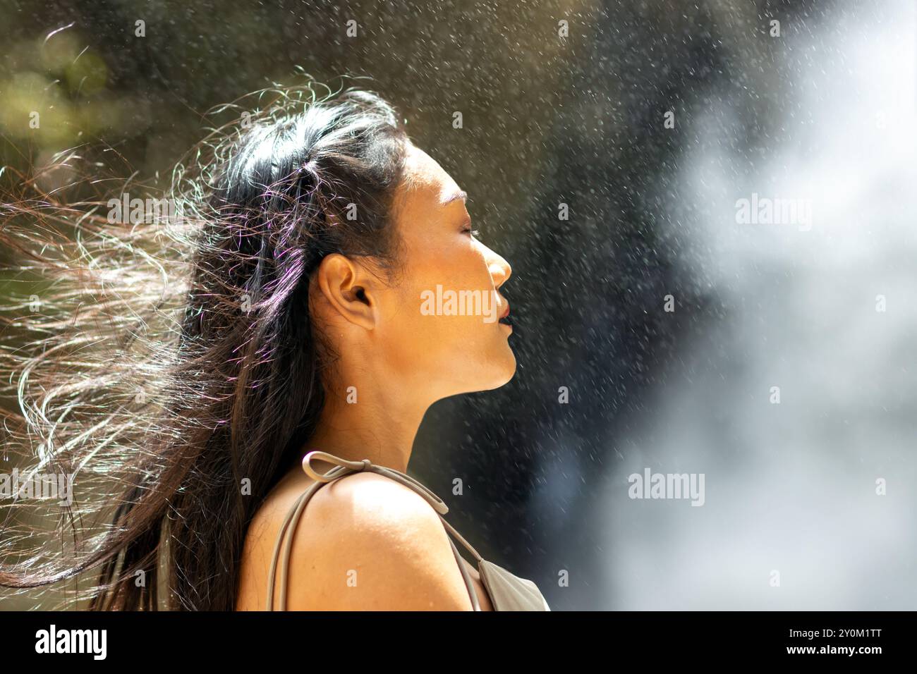 A dreaming woman stands in front of a waterfall with water drops around ...