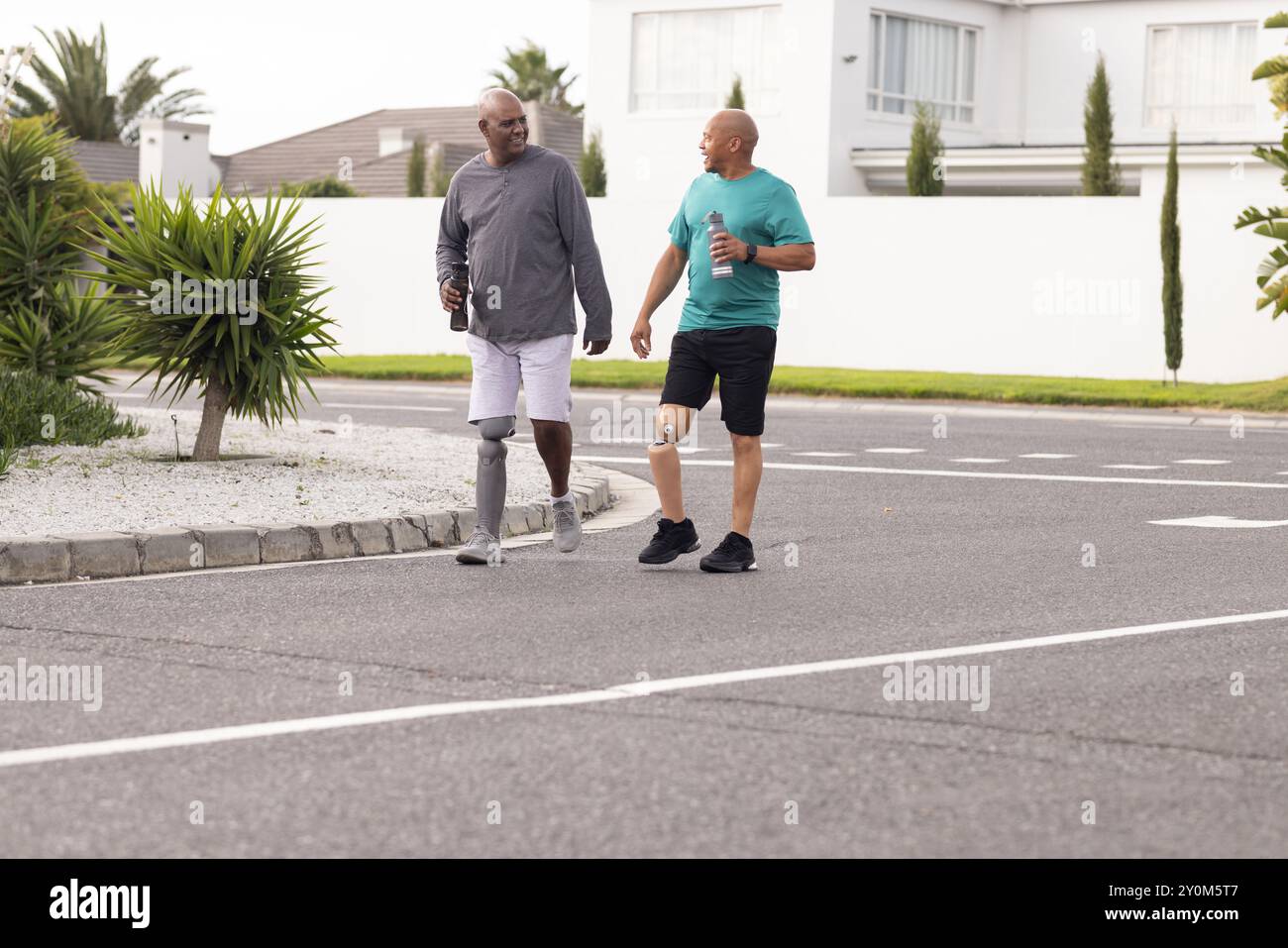 Exercising outdoors, two men with prosthetic legs walking together with ...