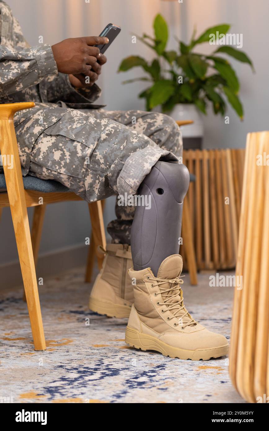 Sitting in chair, soldier with prosthetic leg using smartphone indoors ...
