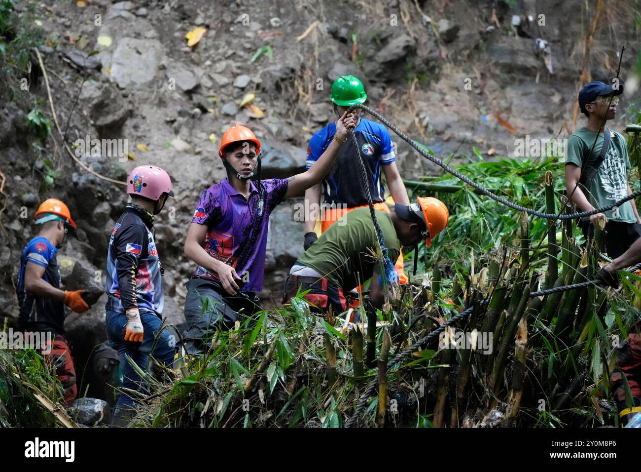 Volunteers and rescuers hold a rope as they move debris during search ...