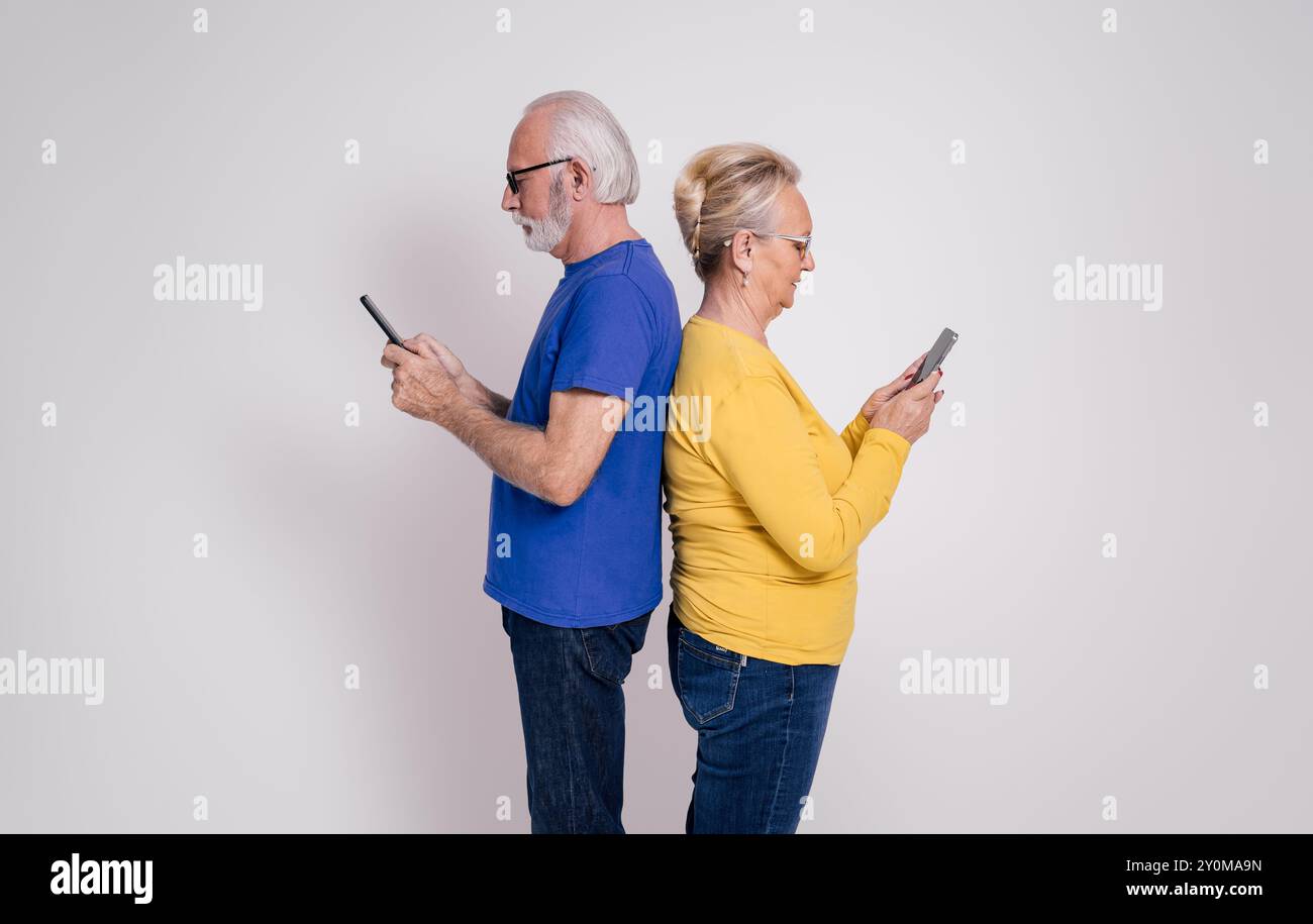 Side view of senior couple texting over smart phones and standing back ...