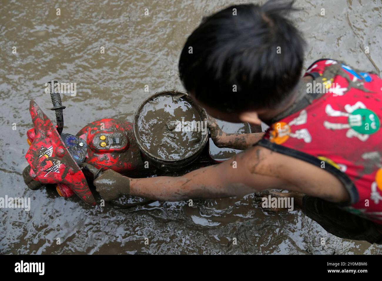 A boy uses a toy bike to collect mud as they clean their flood-hit ...