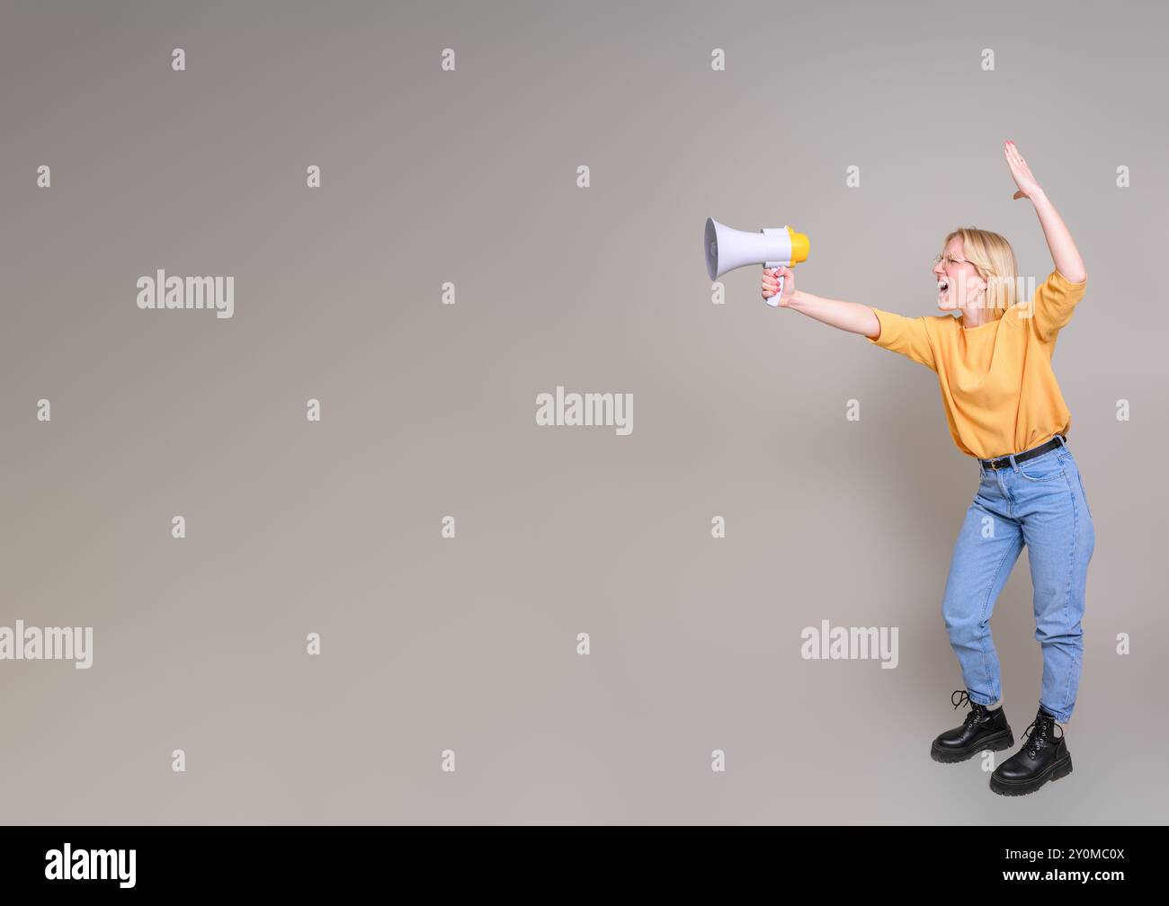 Full length of female speaker with arm raised shouting over megaphone ...