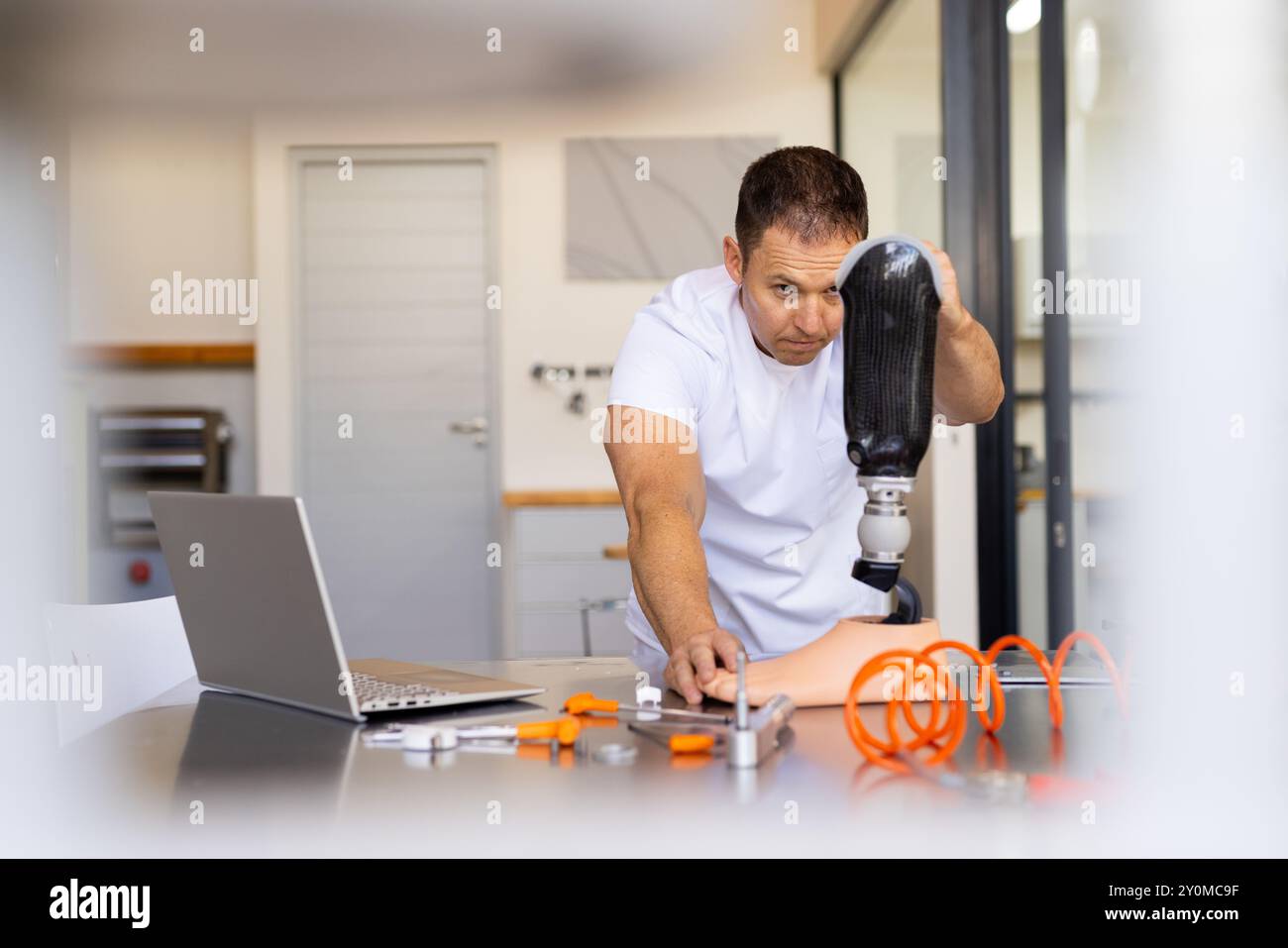 Man in prosthetic lab working on artificial limb with laptop on table ...