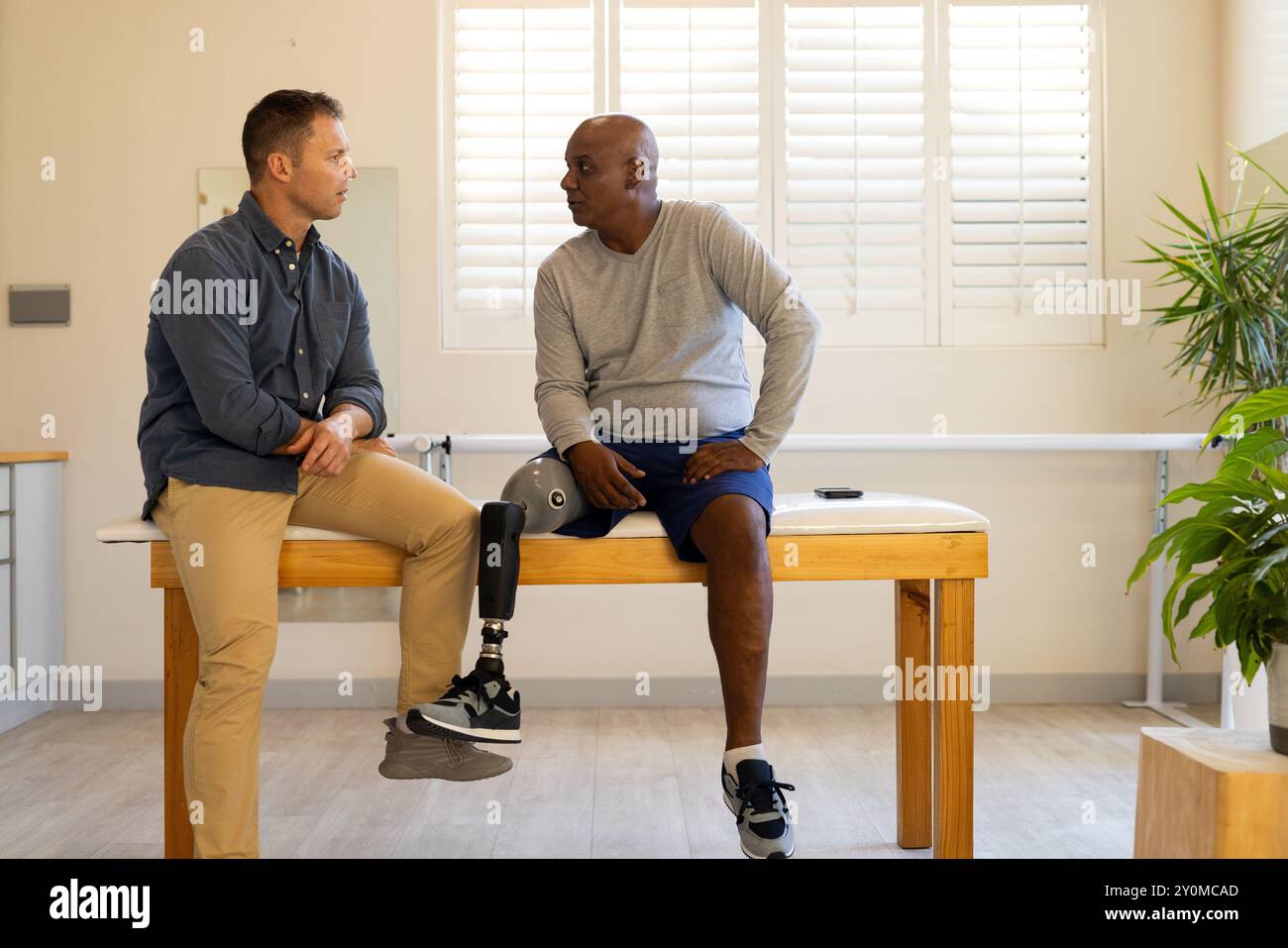 Discussing prosthetic leg, two men sitting on table in medical clinic ...