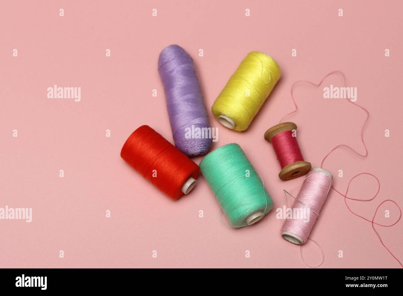 Spools of thread and needles on a pink background with space for text ...