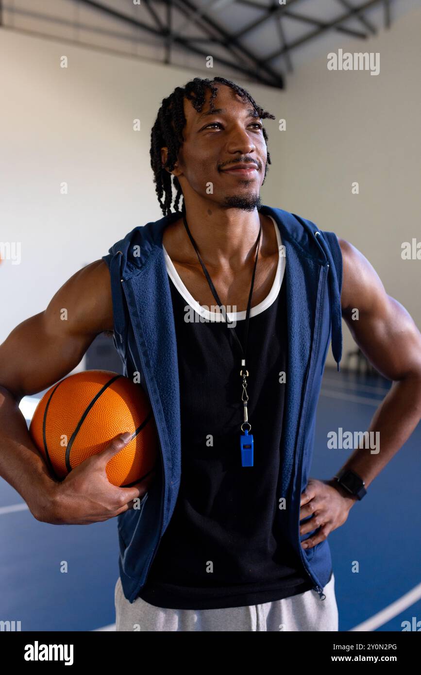 Holding basketball, coach standing confidently in school gymnasium ...