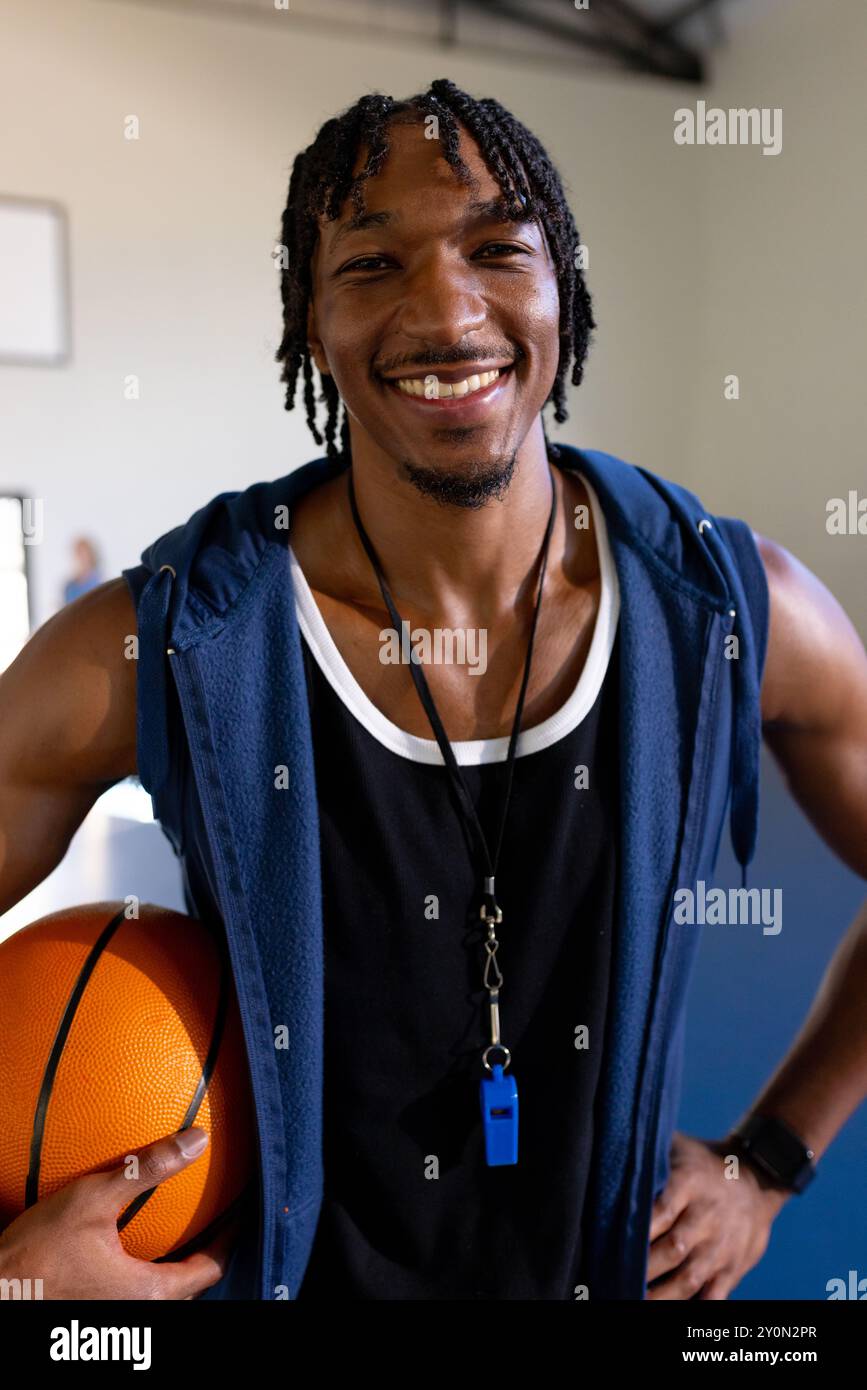 Smiling male african American basketball coach holding basketball and ...