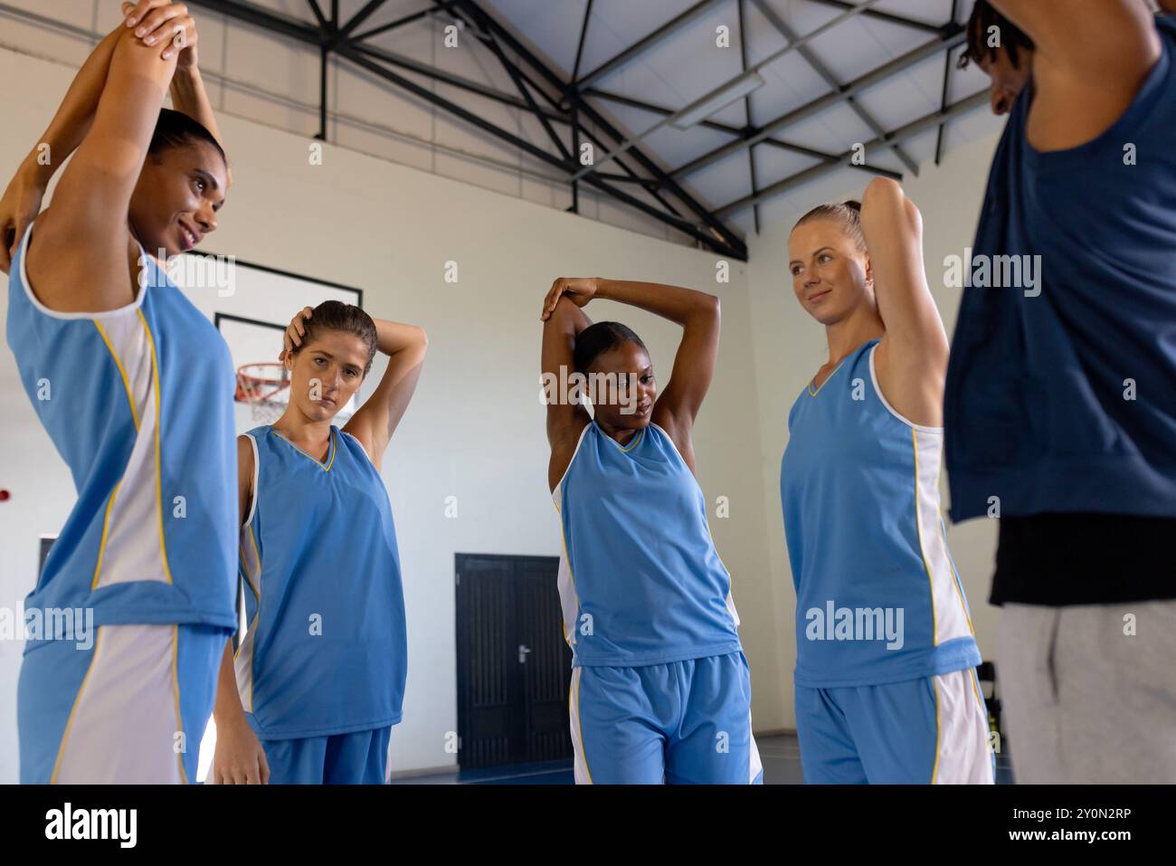 Female basketball players stretching arms together in gym before ...