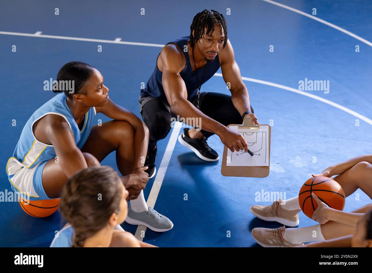 Basketball male coach discussing strategy with female players on court ...