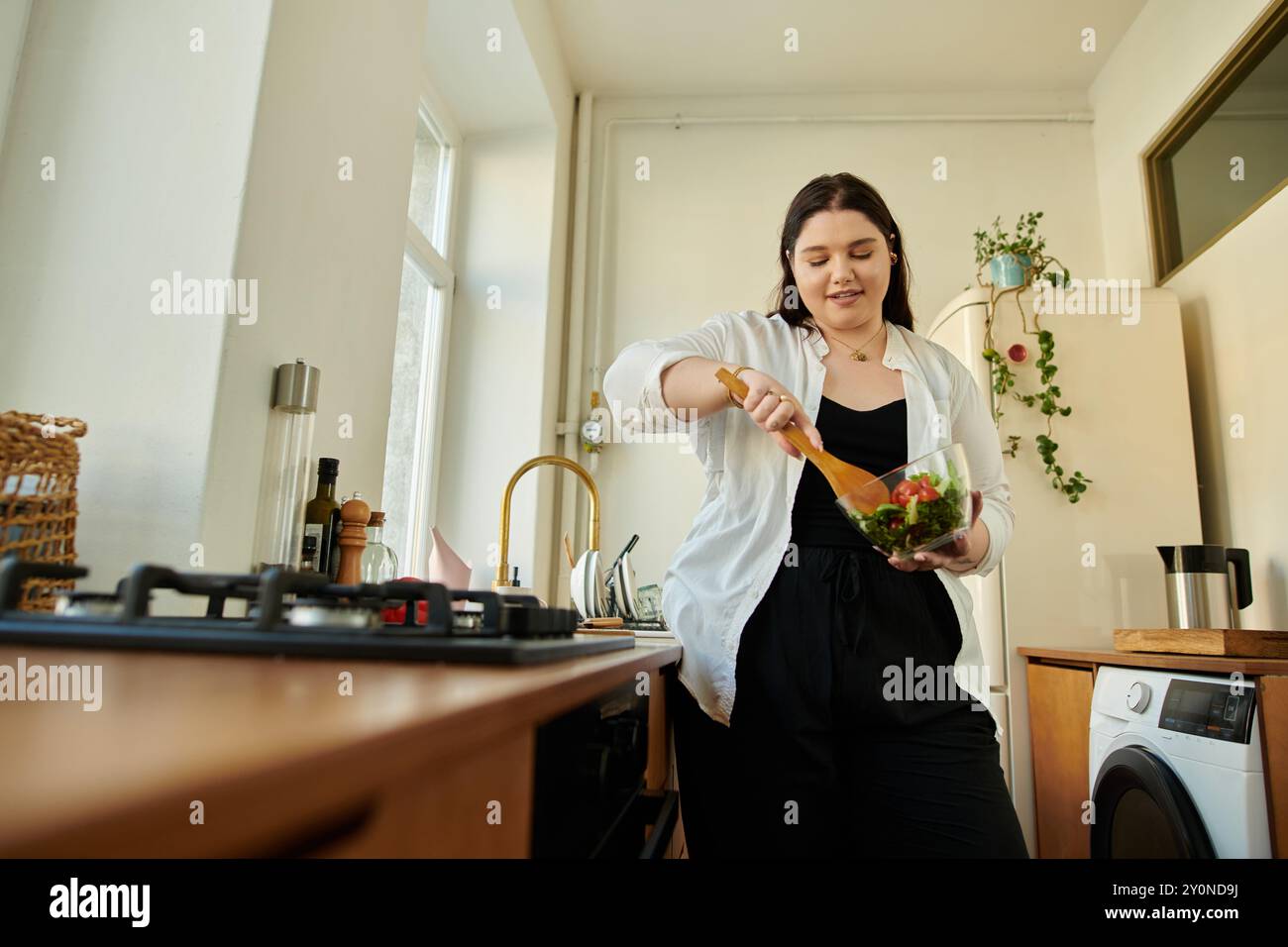 A beautiful woman joyfully mixes fresh ingredients in her kitchen Stock ...