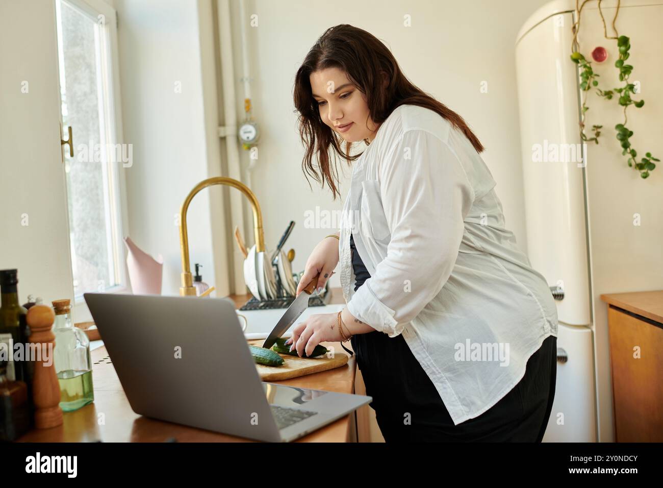 A plus size woman joyfully prepares a meal while following a recipe ...