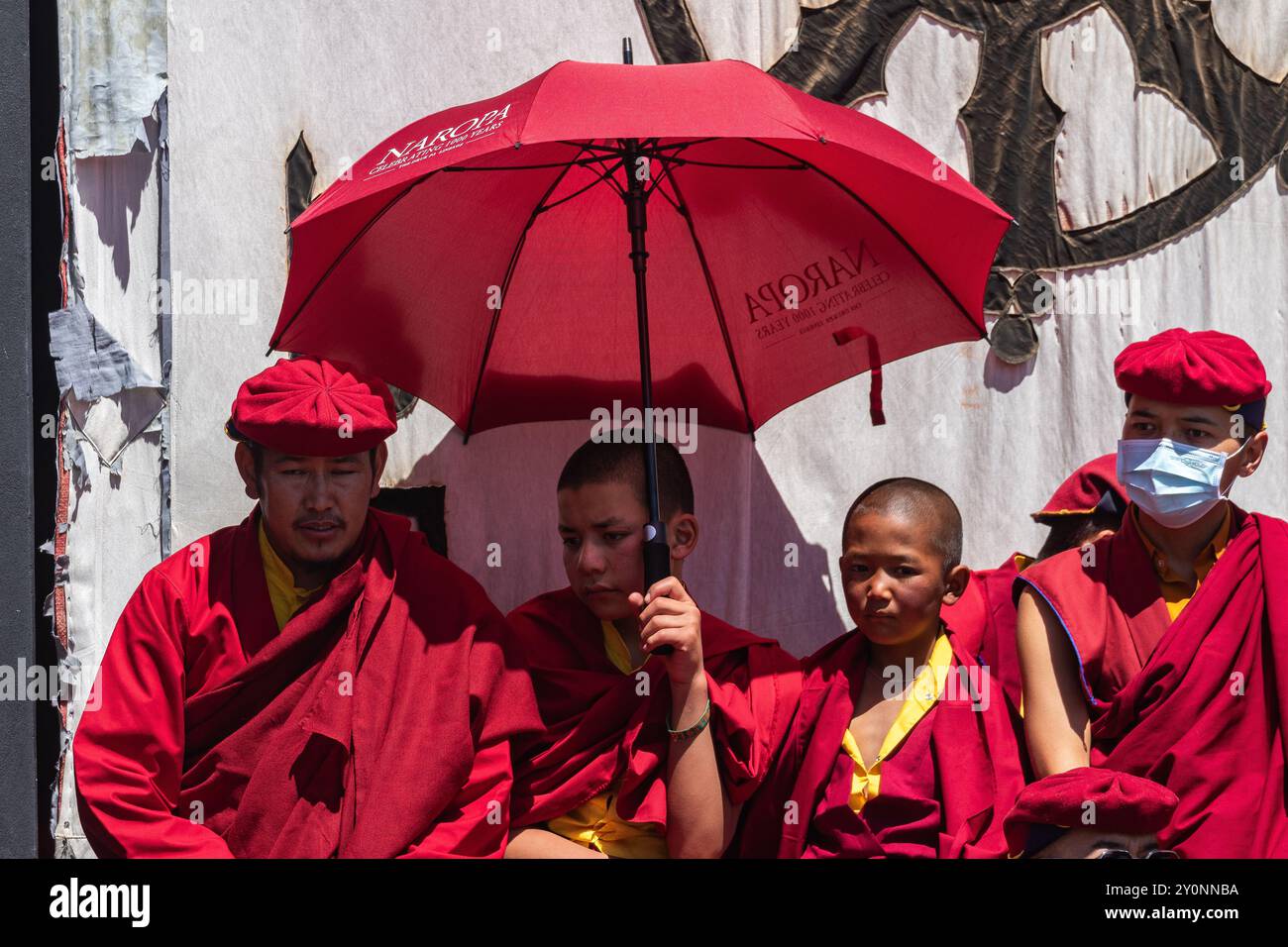 Tibetan monks wearing red robes and using an umbrella, sitting together ...