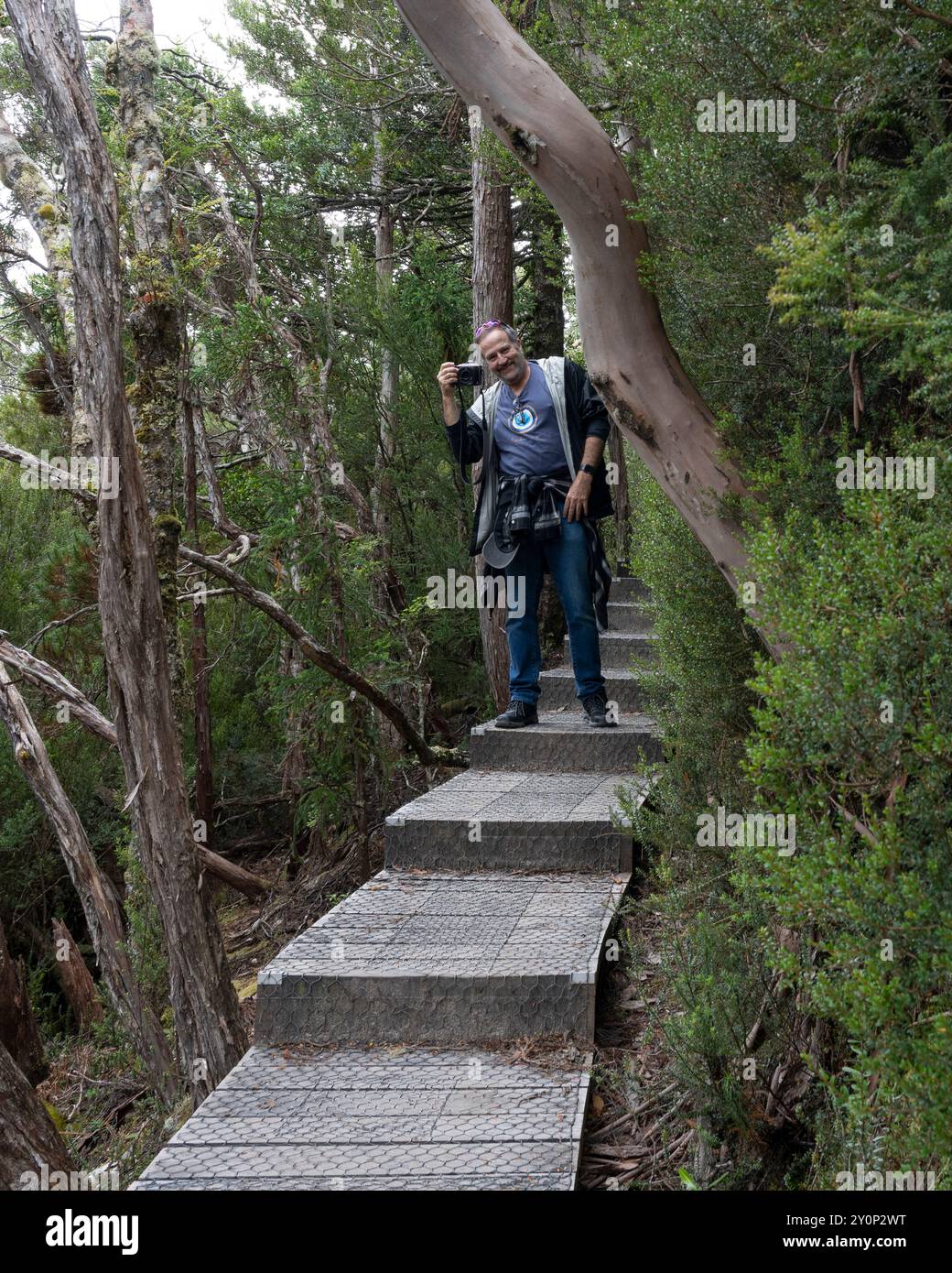 Front view of a male photographer walking along a wooden trail in the ...