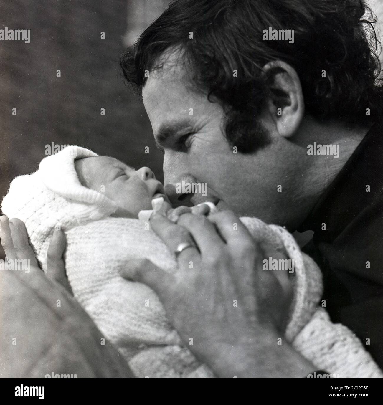1970s, historical, outside, a new father holding his baby, wrapped in a ...