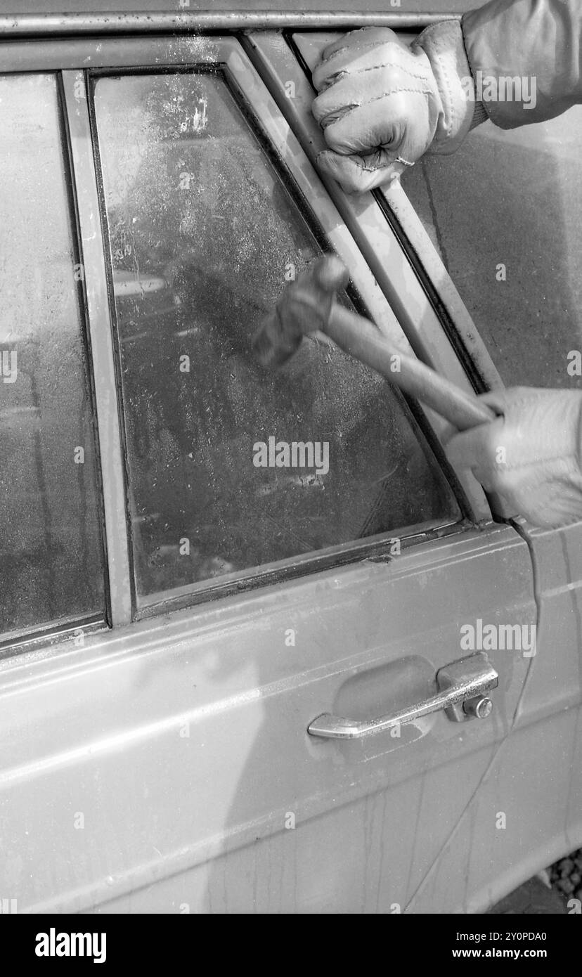 1970s, a gloved car thief using a hammer to smash a rear side car ...