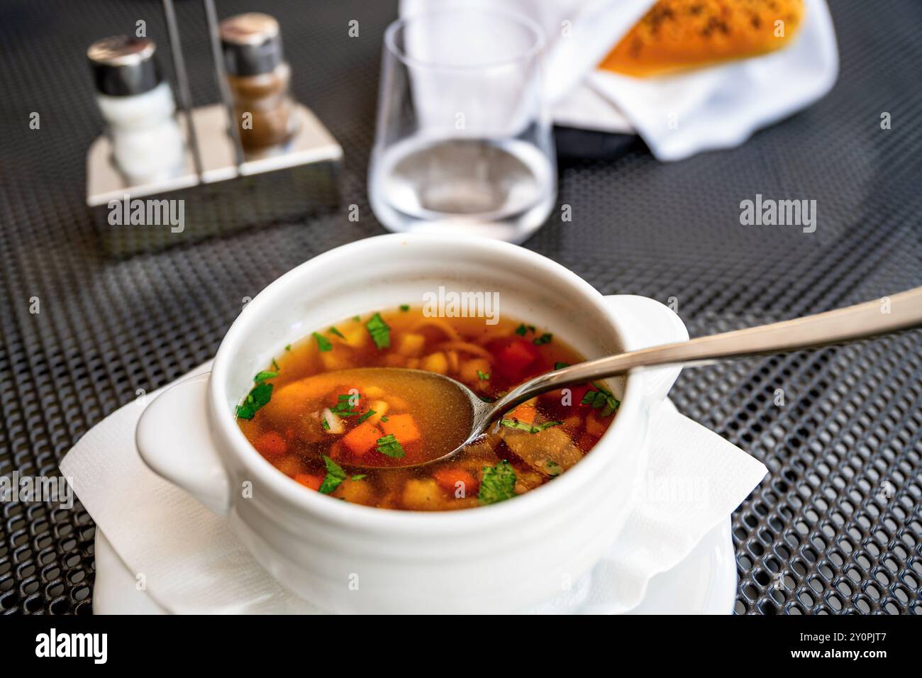 Strong broth with vegetable in small white soup bowl with spoon,glass ...