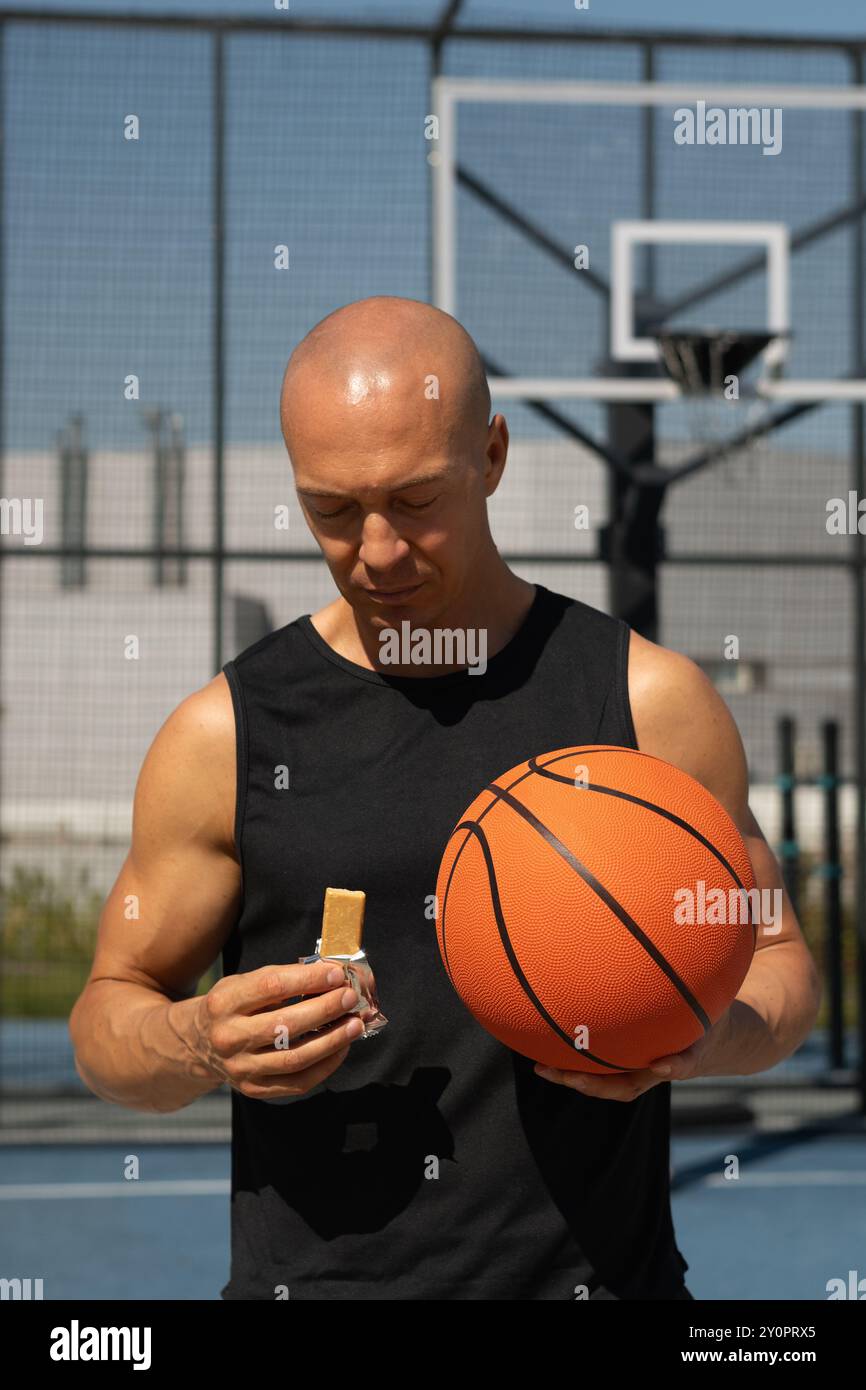 Portrait of basketball player man eating energy bar. Muscular athlete ...