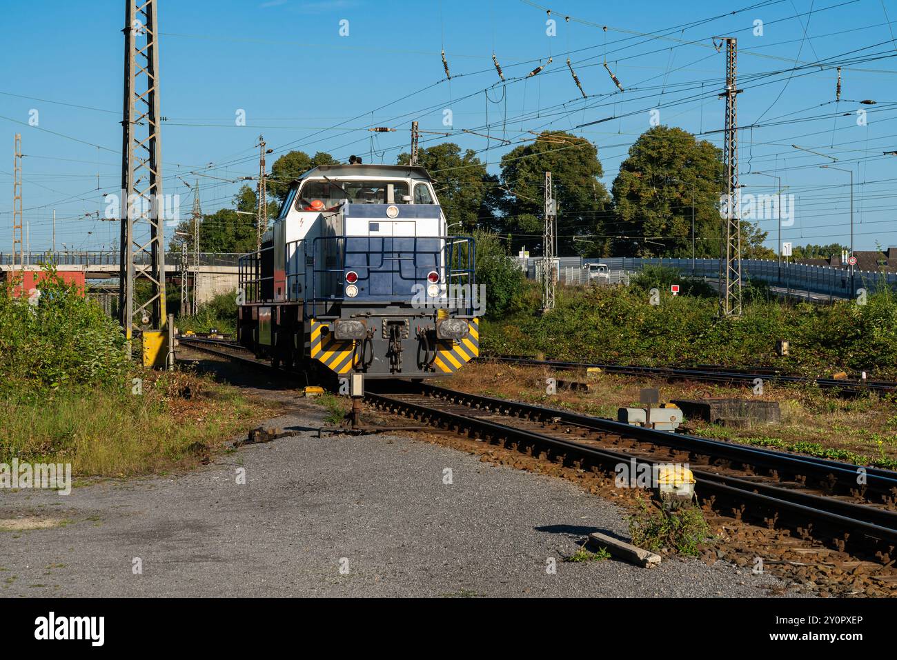 A white and blue train engine on railway tracks amidst a green, rural ...
