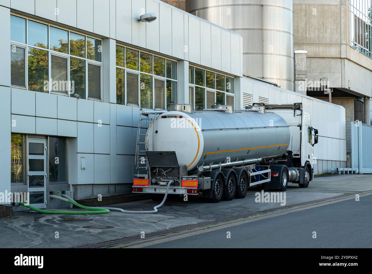 A tanker truck with hoses connected to a building, facilitating the ...