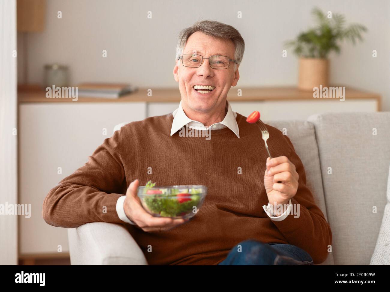 Elderly man eating vegetable salad smiling sitting on sofa Stock Photo ...