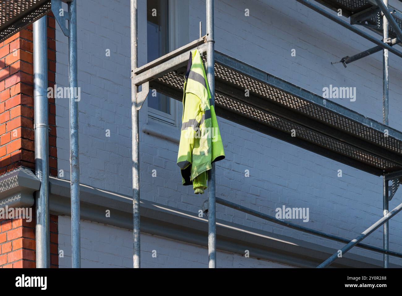 A bright yellow safety vest is hanging from scaffolding at a ...