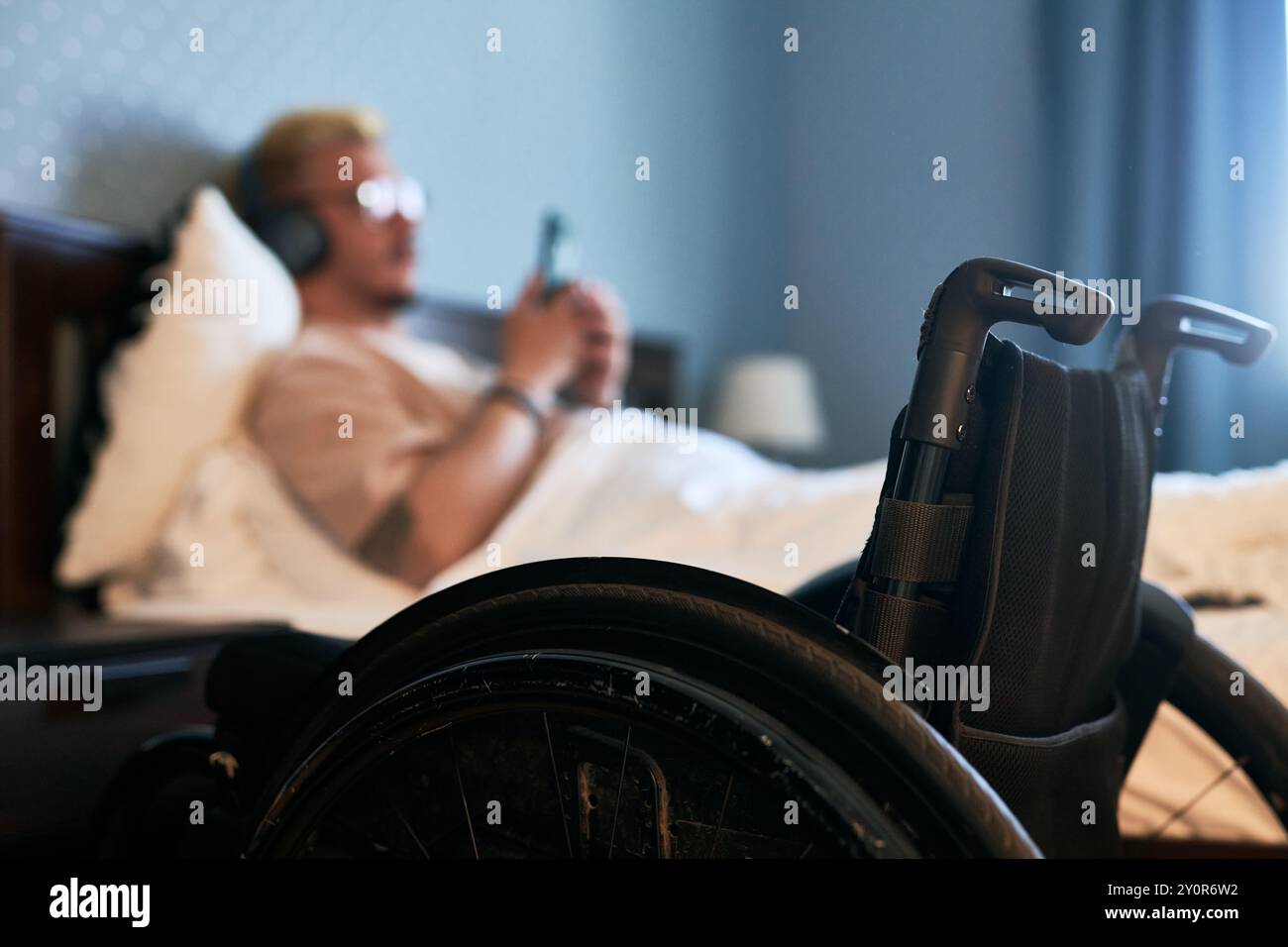 Caucasian person using headphones and phone while resting on bed next ...