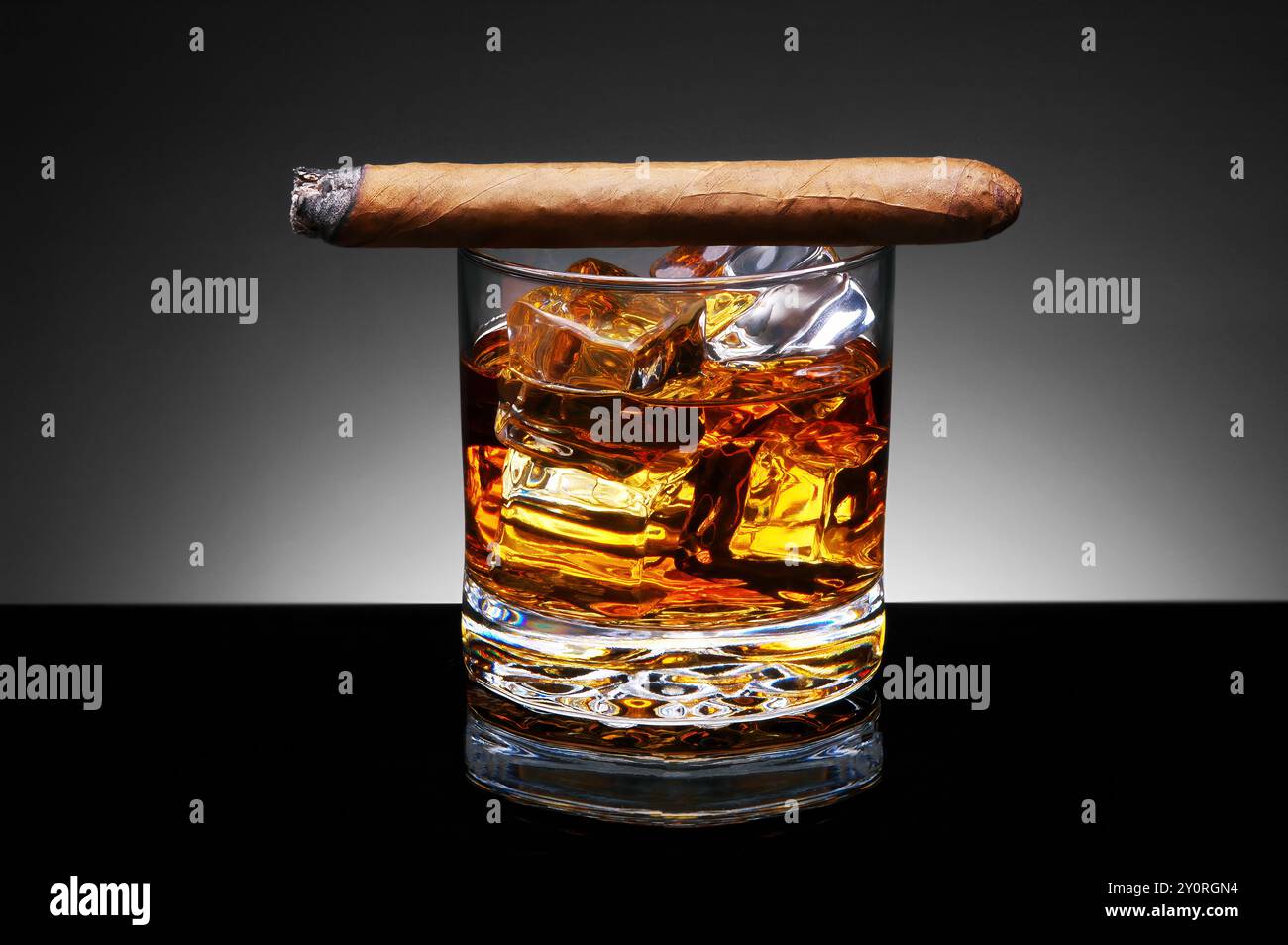 A lit cigar resting on top of a glass of whiskey and ice cubes over a ...