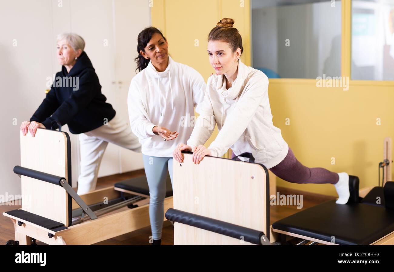 Hispanic female pilates instructor helping girl exercising on reformer ...