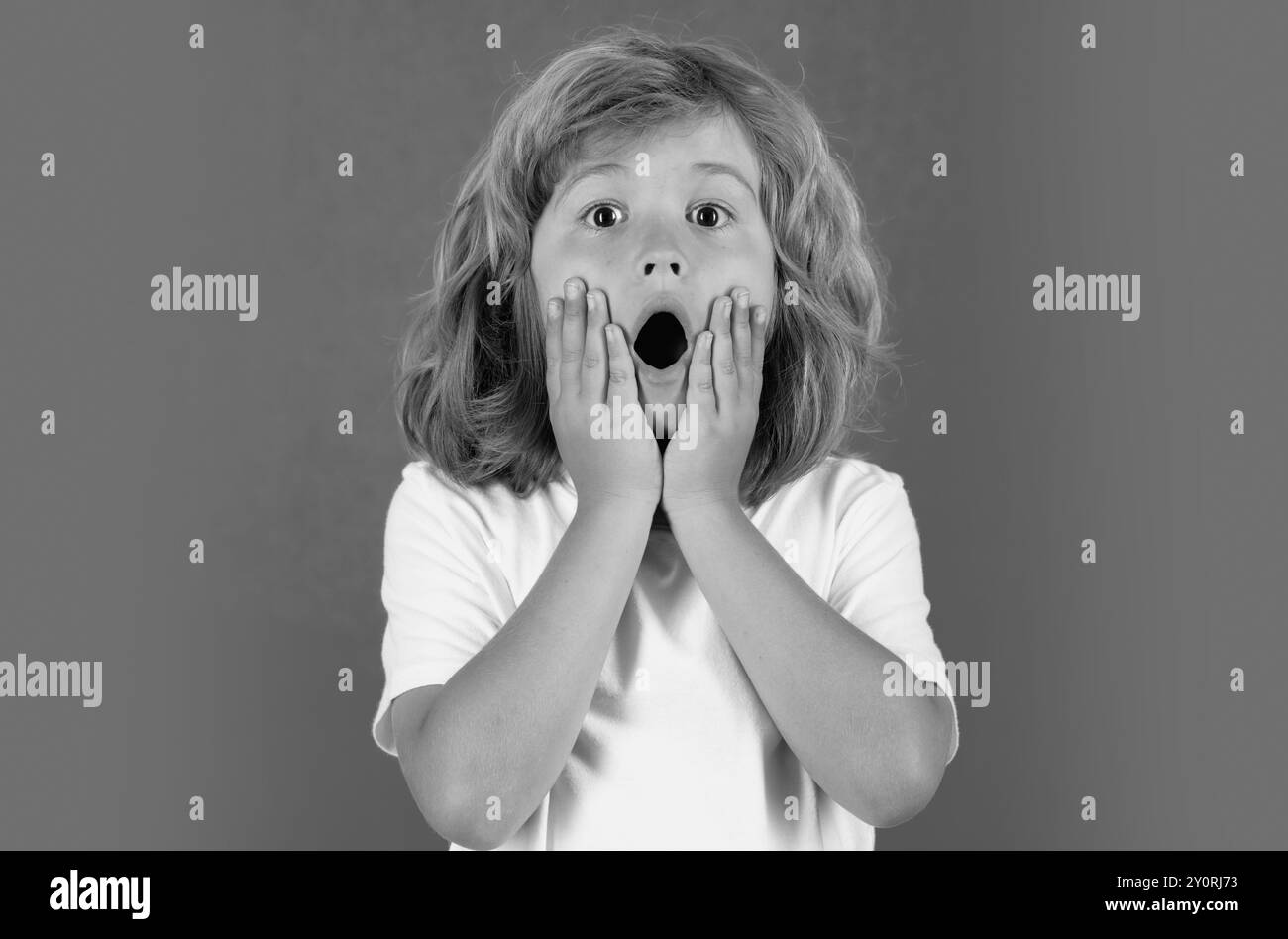 Shocked child boy keeping hands near cheek with open mouth on studio ...