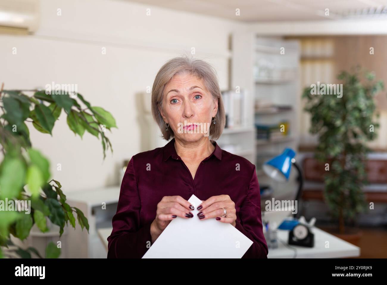 Upset elderly female office employee holding paper document Stock Photo ...