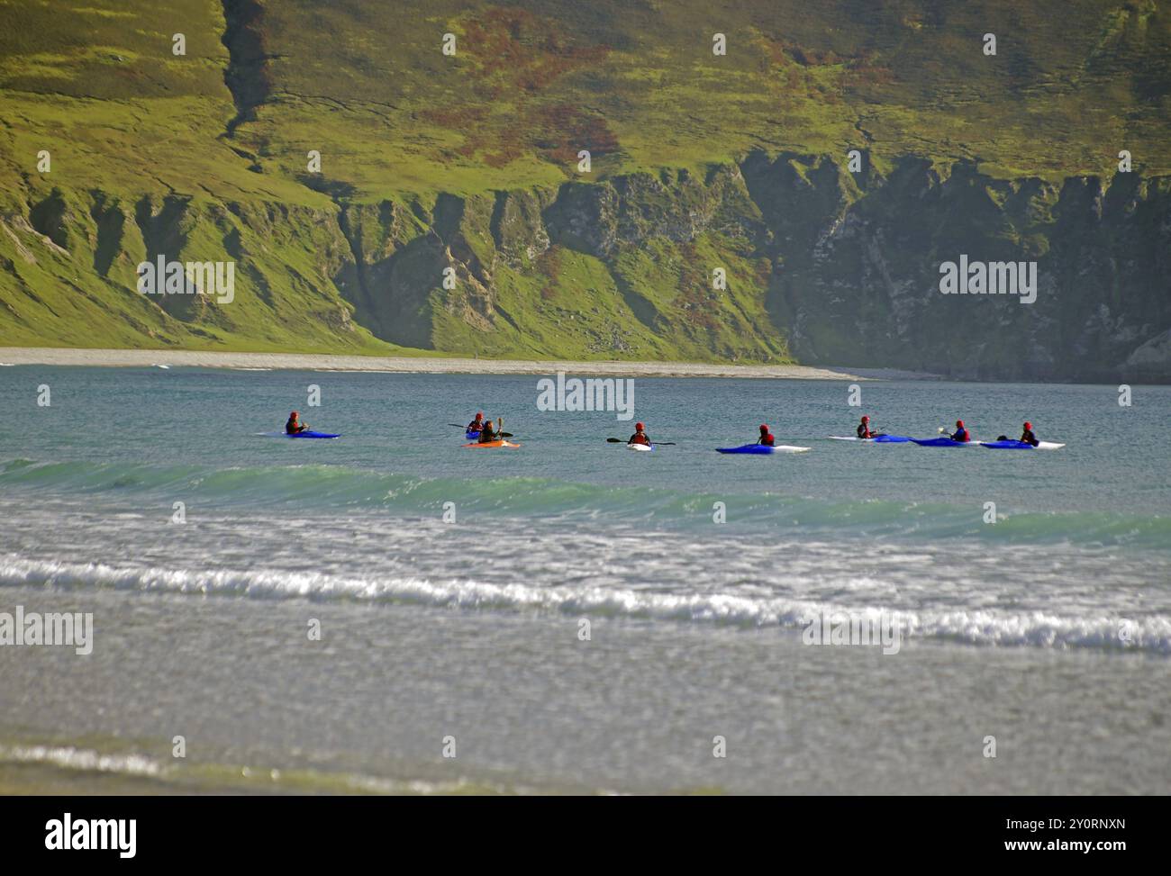 Group of surfers on their boards on the sea near rocky shore, Achill ...