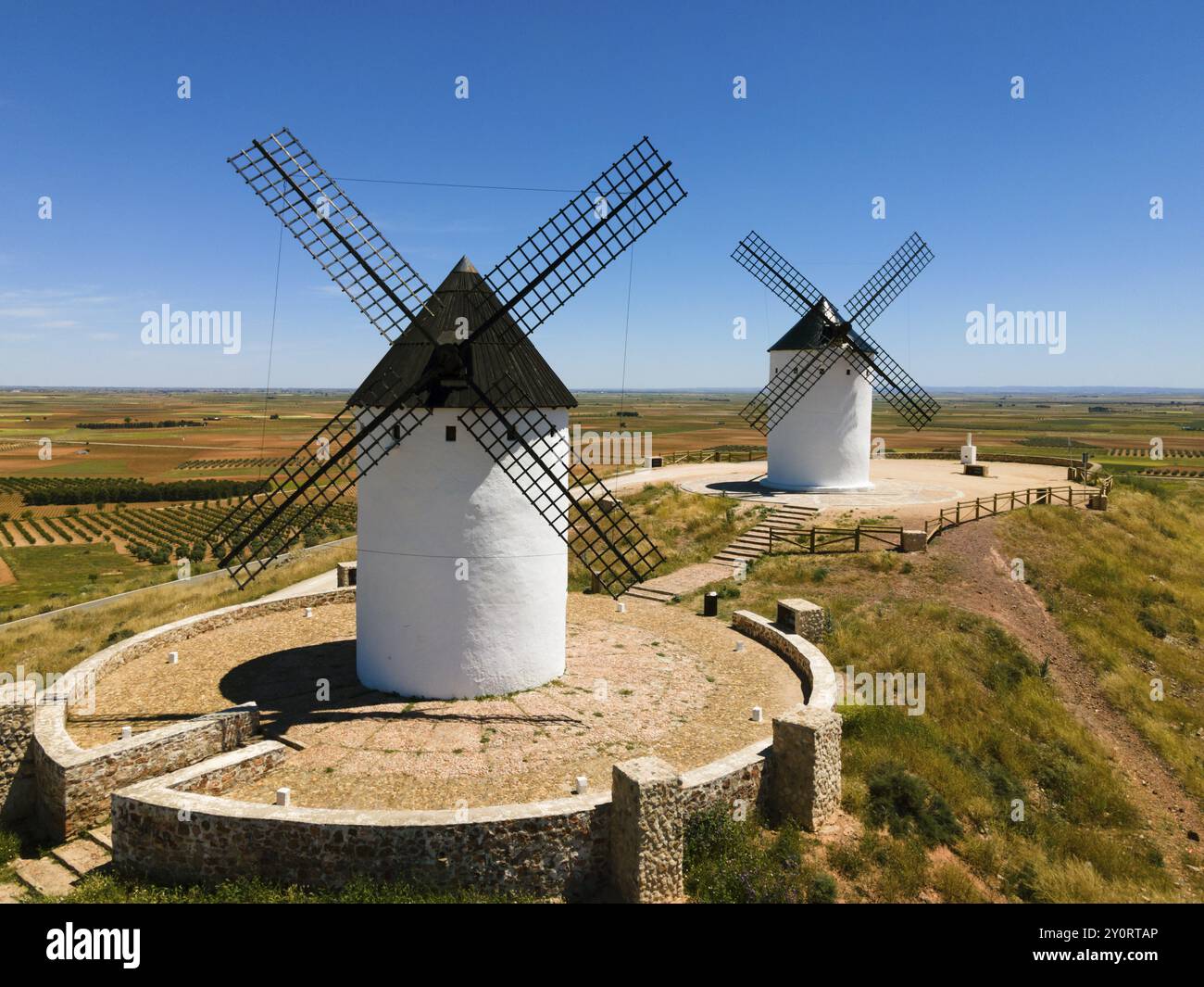 Two white windmills with black roofs on a hill surrounded by stone walls and wide fields, aerial ...