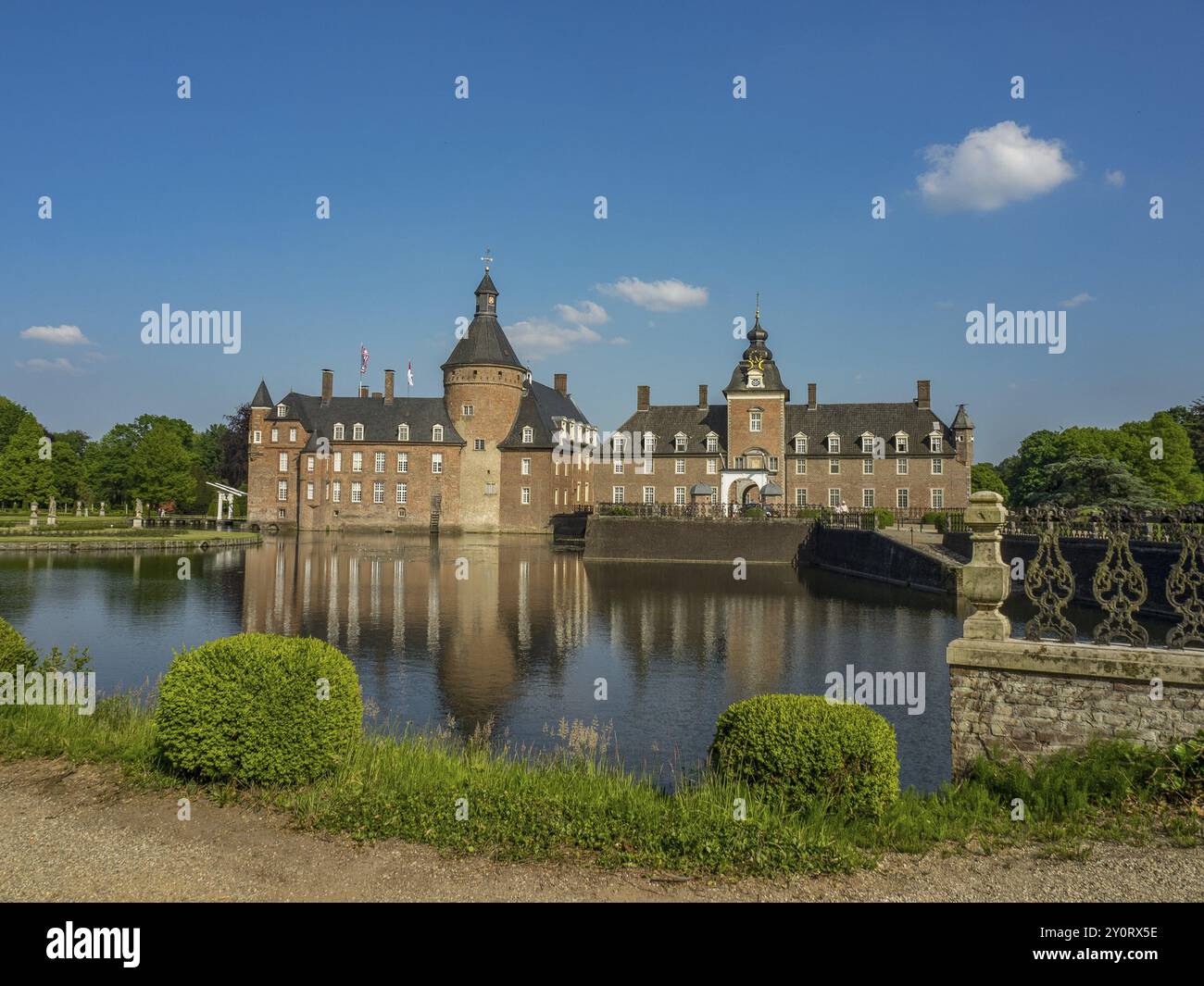 A large brick castle with moat and reflections, surrounded by greenery ...