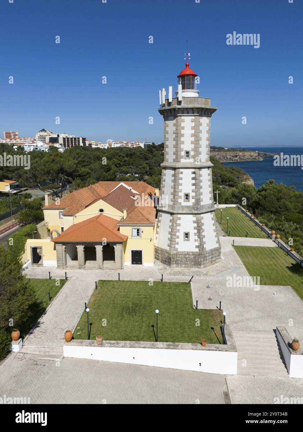 A lighthouse with a red top next to a yellow building, surrounded by a ...