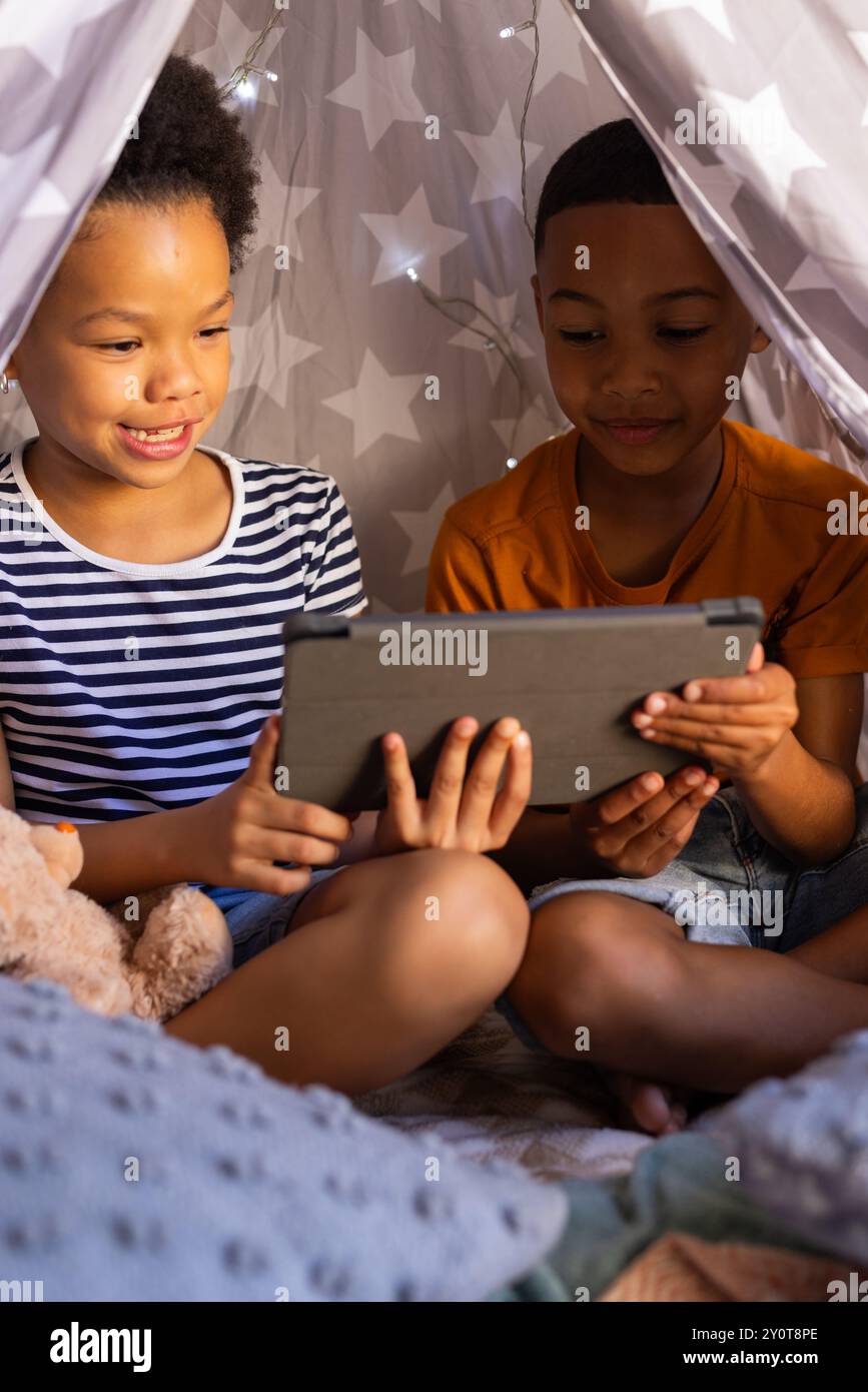 brother and sister sitting in blanket fort, watching tablet together ...