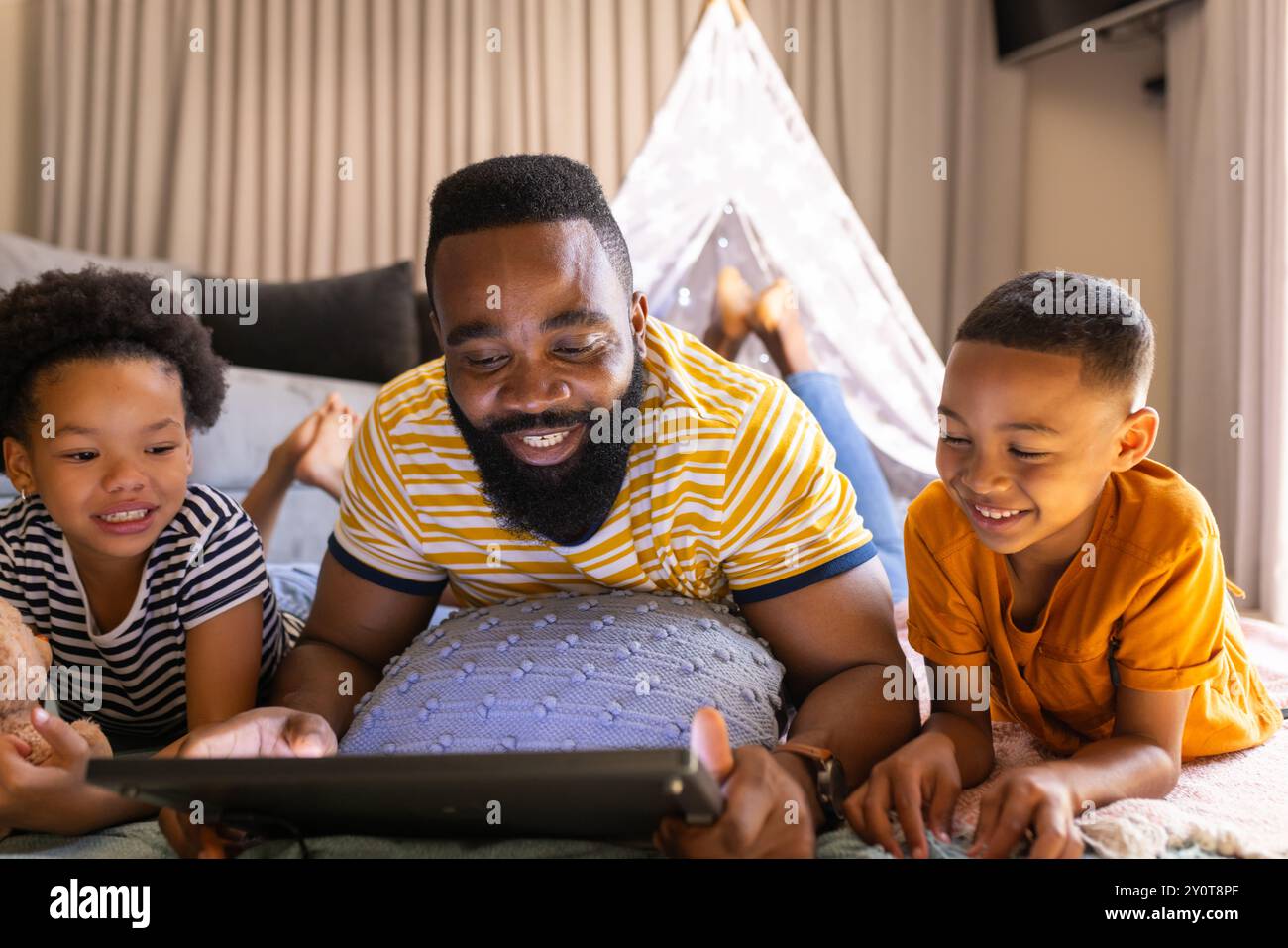 Using tablet, father and brother and sister lying on bed, enjoying ...