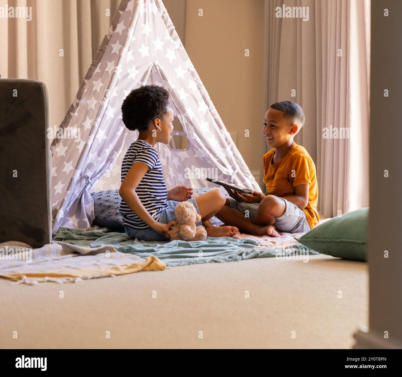 Playing in tent, young brother and sister reading book and holding ...