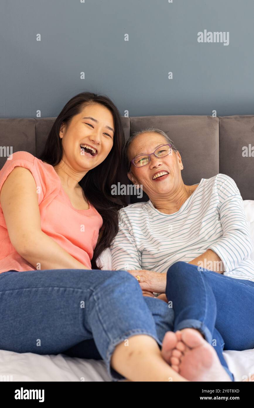 Laughing together, asian grandmother and granddaughter relaxing on bed, enjoying quality family ...