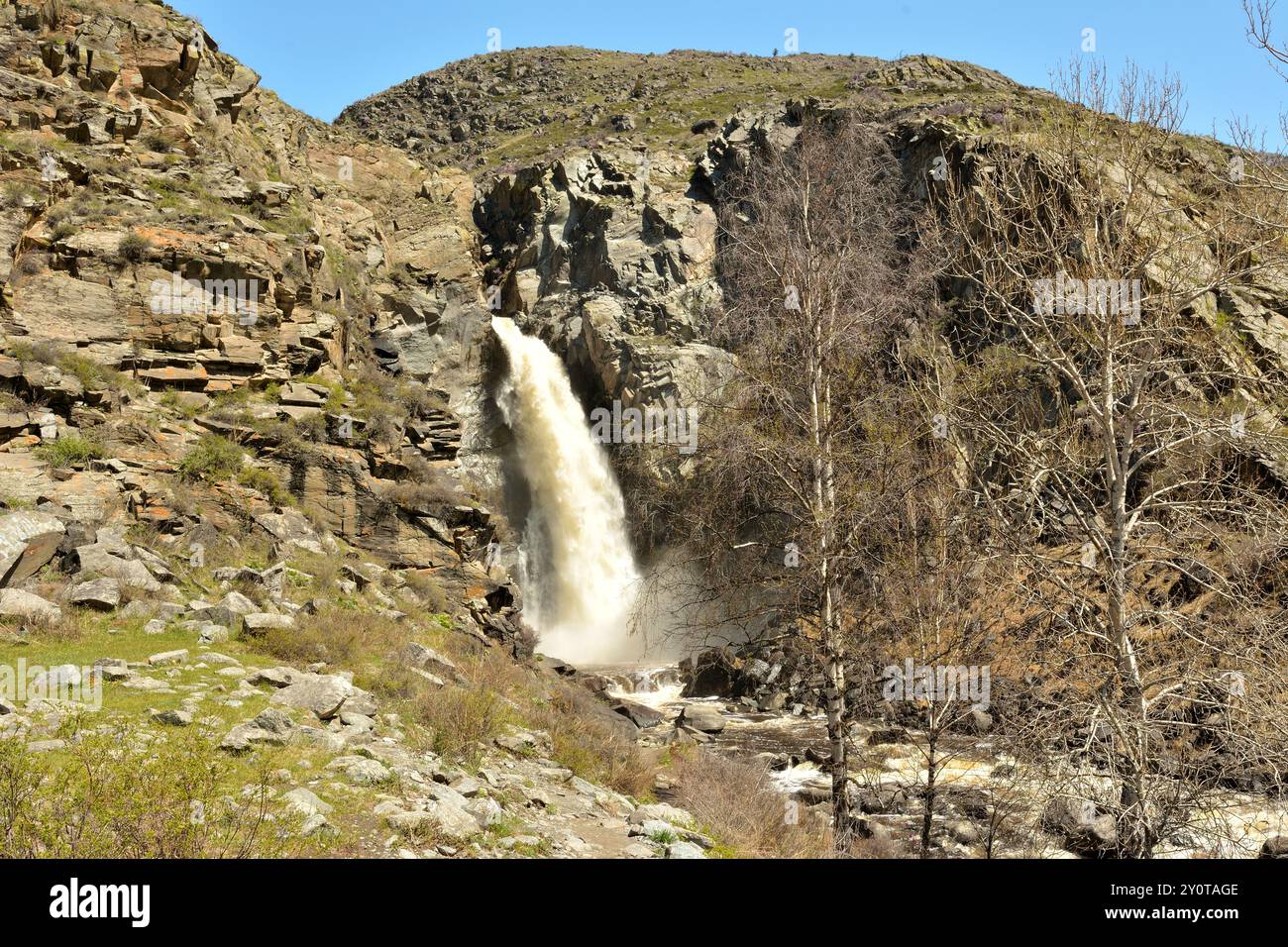 A stormy stream of water flows from a crevice in the mountains onto a ...