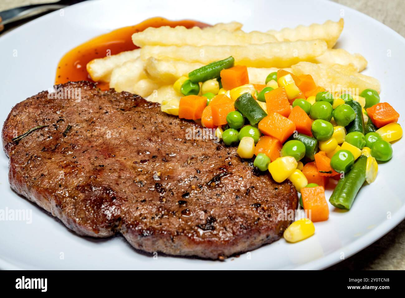 A plate of food with a piece of picanha meat, vegetable mix, and french ...