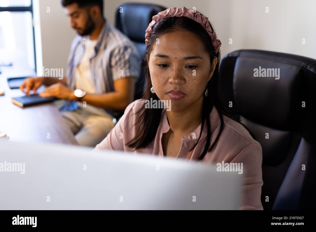 Working in office, woman using computer while colleague taking notes in ...