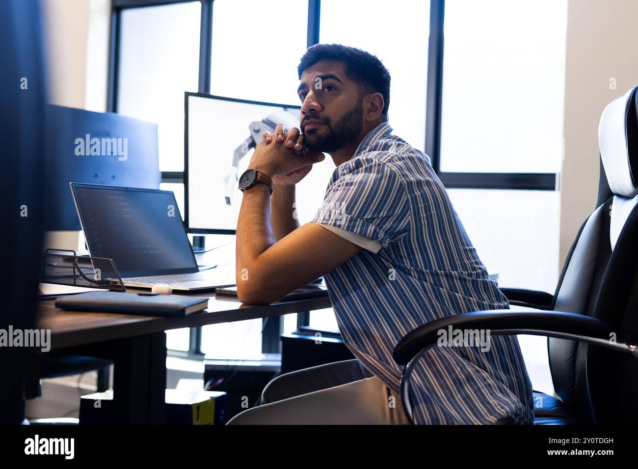 Thinking deeply, Indian man sitting at desk with laptop and robotic arm ...