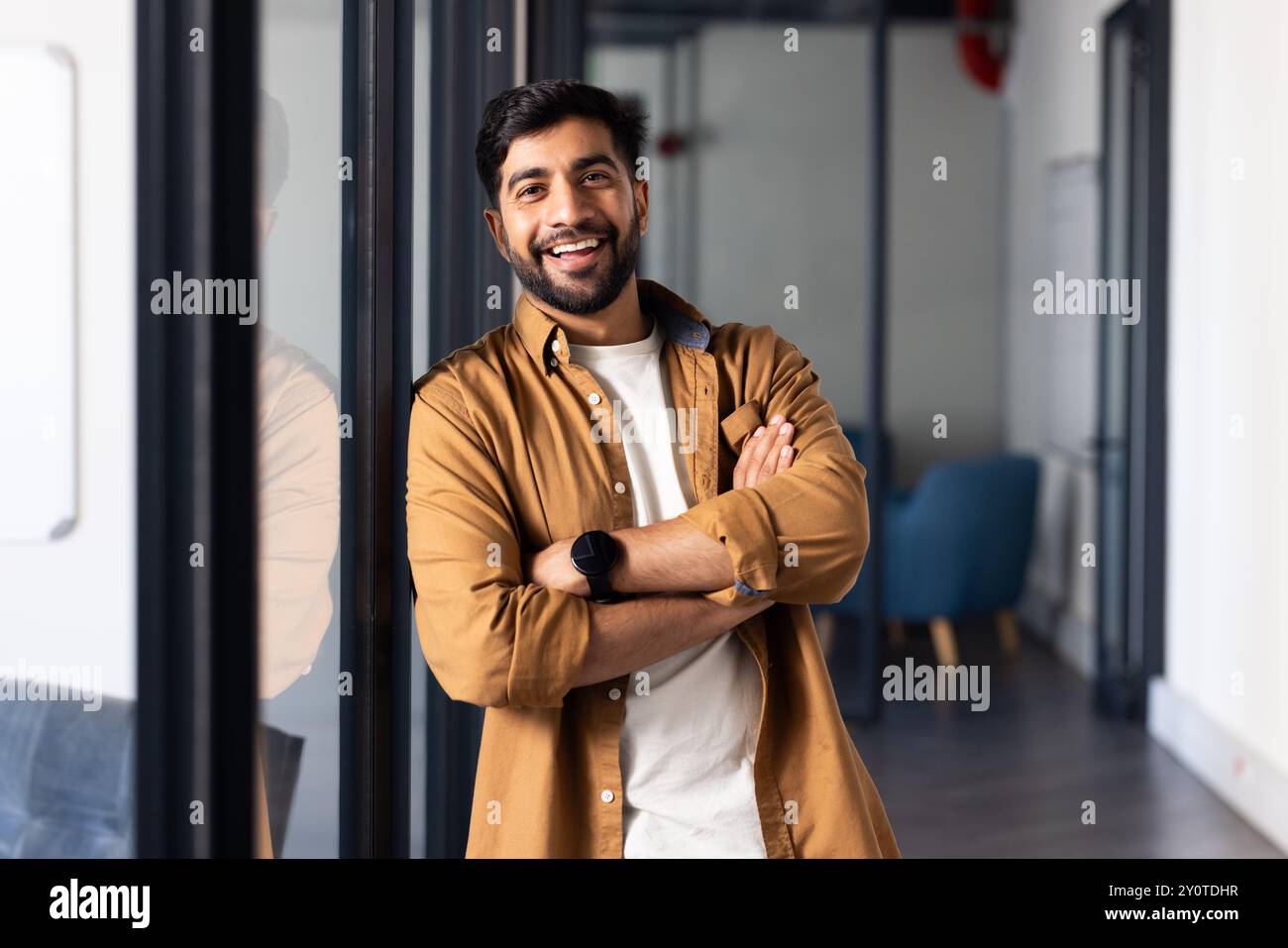 Smiling Indian man in casual attire standing with arms crossed in ...