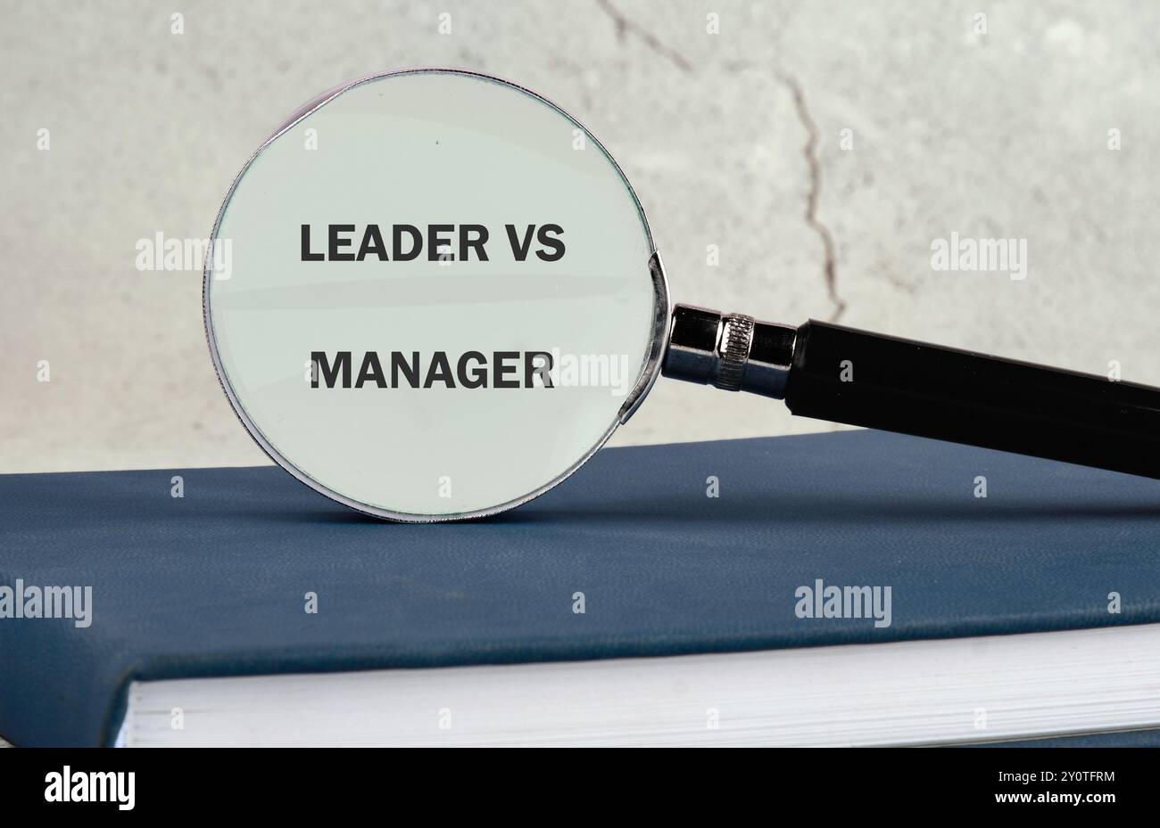 Leader vs manager is shown on a gray background through a magnifying ...