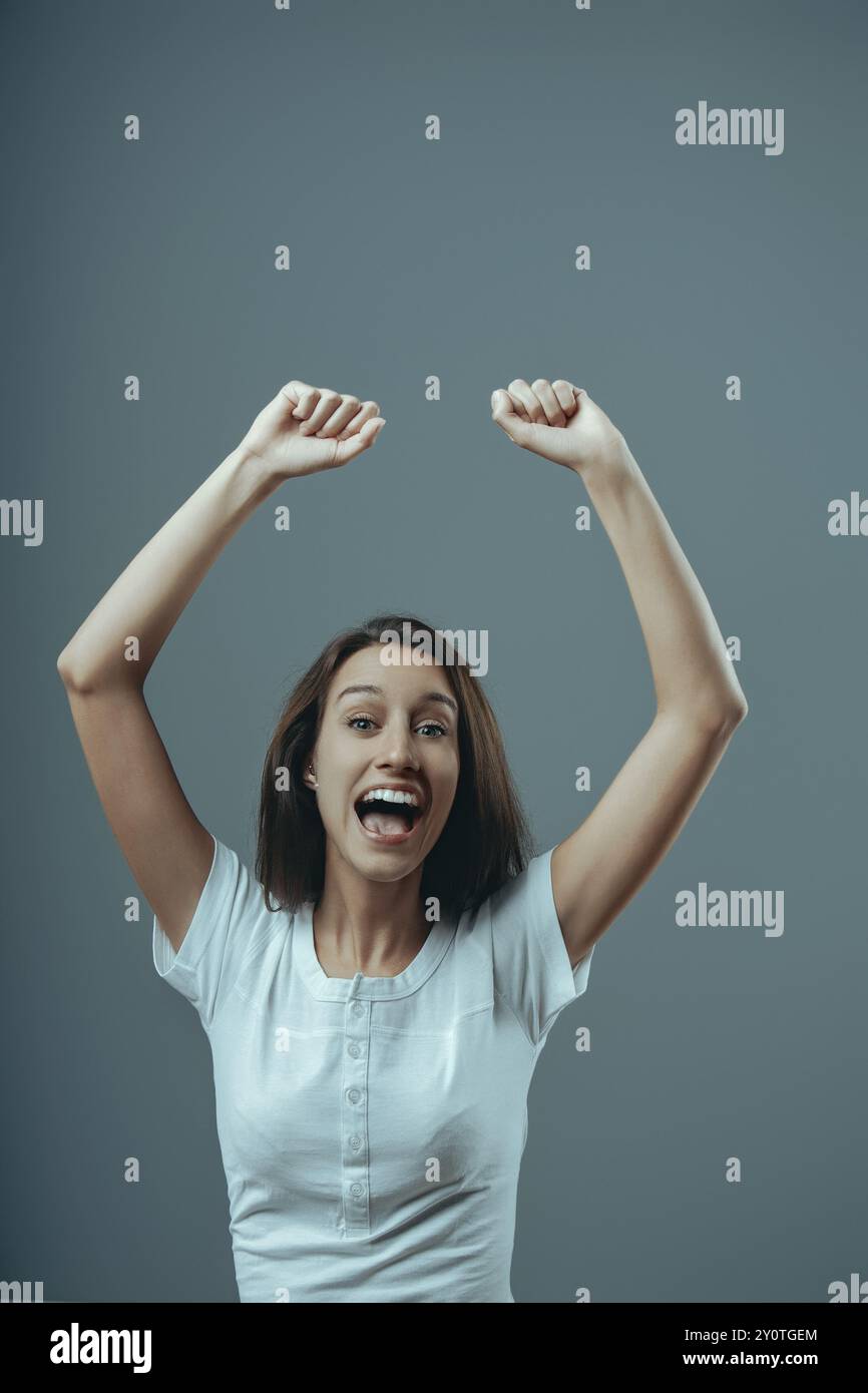 Young woman is screaming of joy with her arms raised and her fists ...