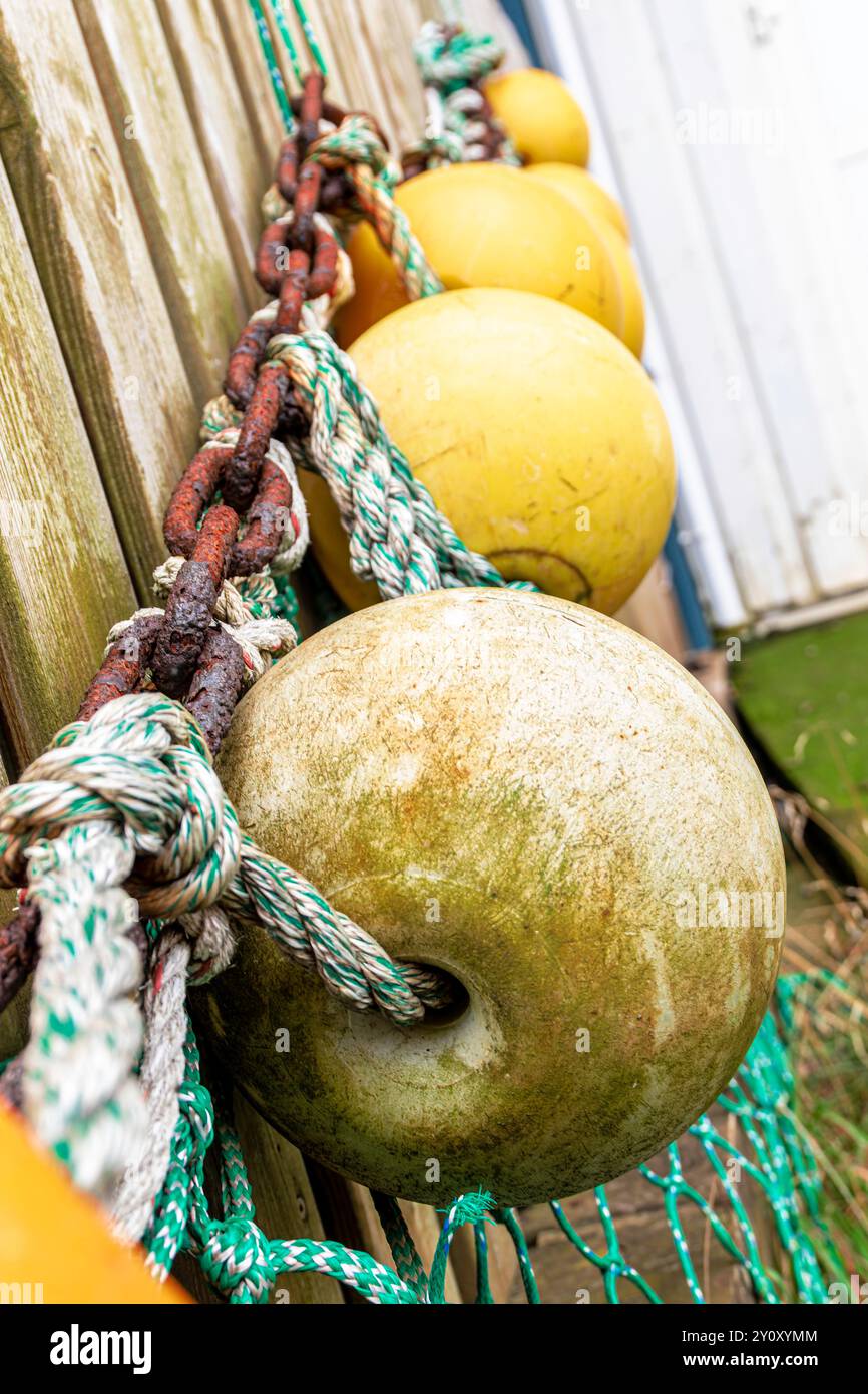 An old fishing net with yellow buoys are hanging from a wooden fence ...