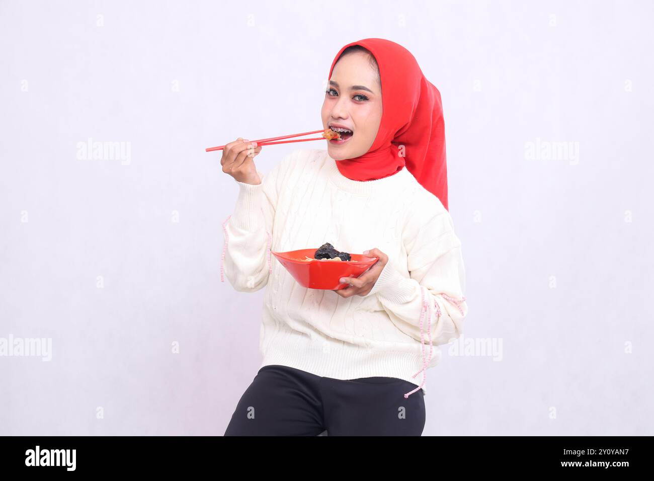 Cheerful indonesia woman wearing a hijab looks at the camera devouring ...