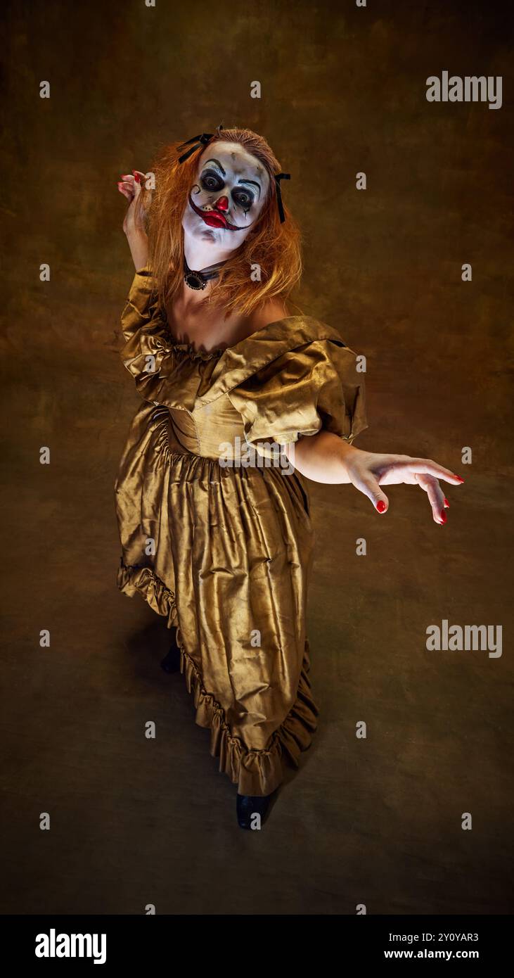 Frightening clown woman in golden gown, raising her hands with wild ...