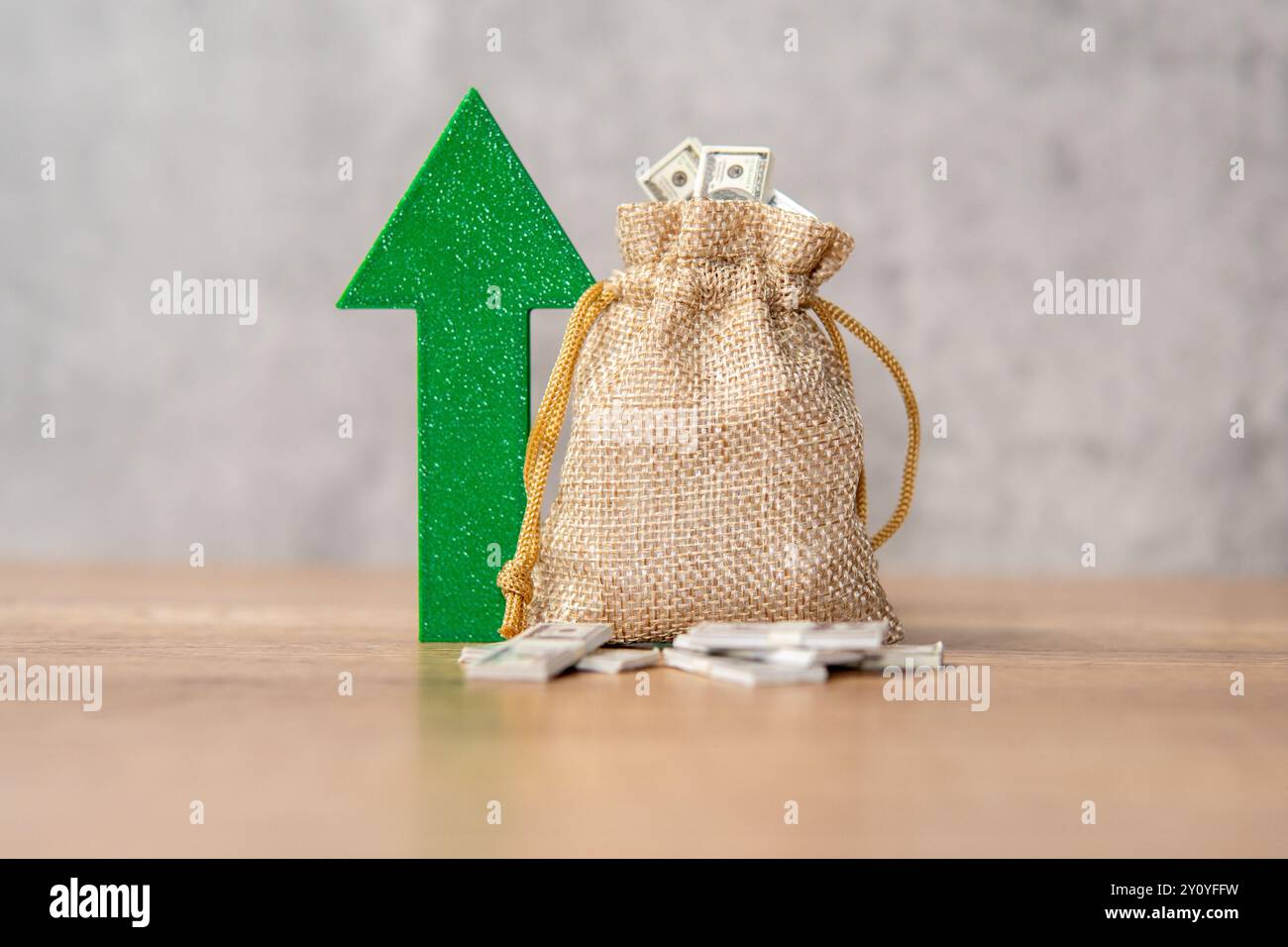 A burlap sack filled with a dollar bills, placed next to a green upward ...